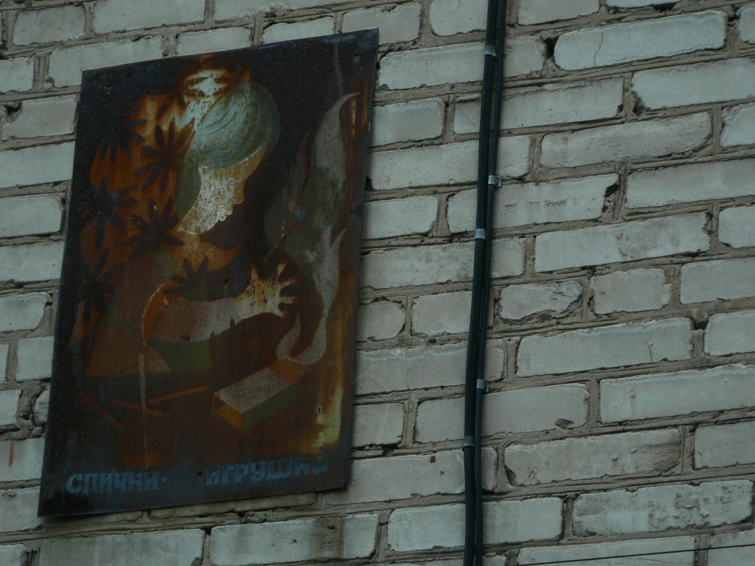 Weathered mural on a brick wall: a cryptic figure under a conduit