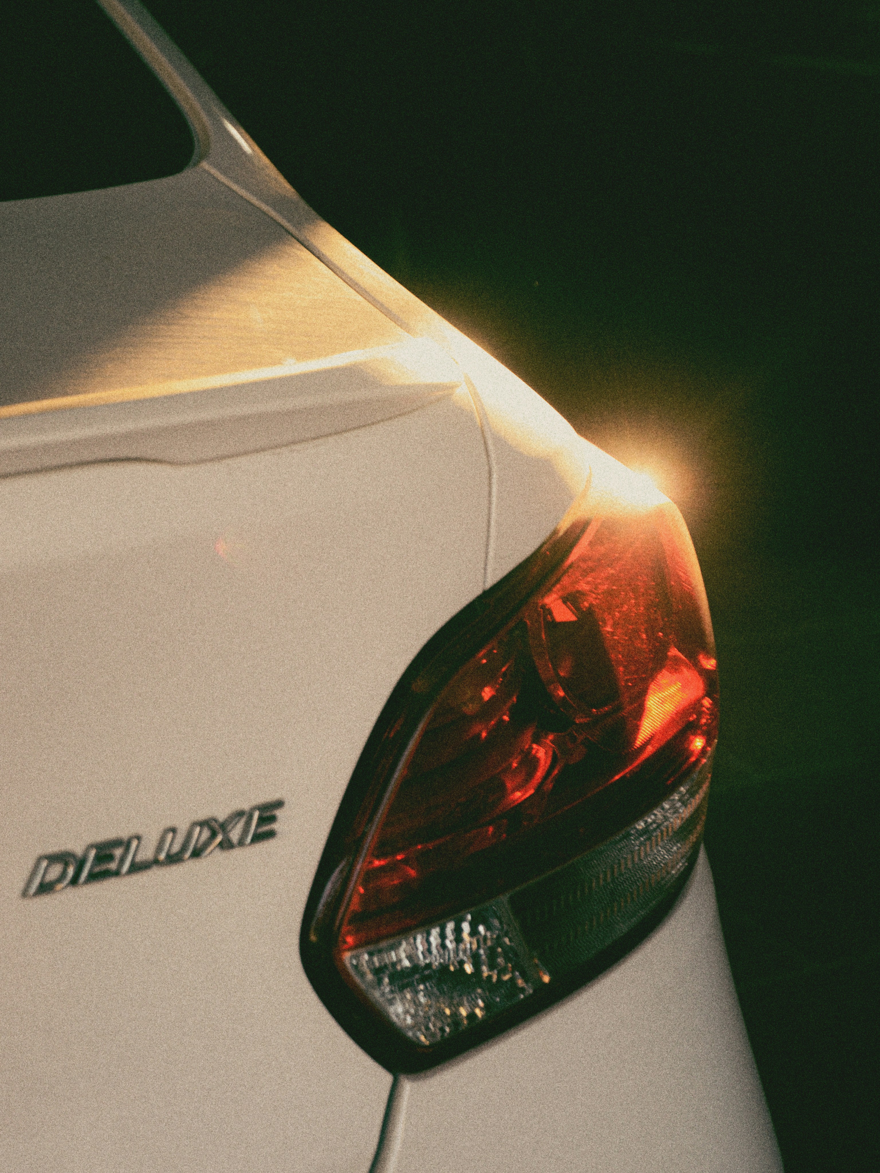Tail Light in Quiet Sunset: The Deluxe Emblem on a White Hatchback
