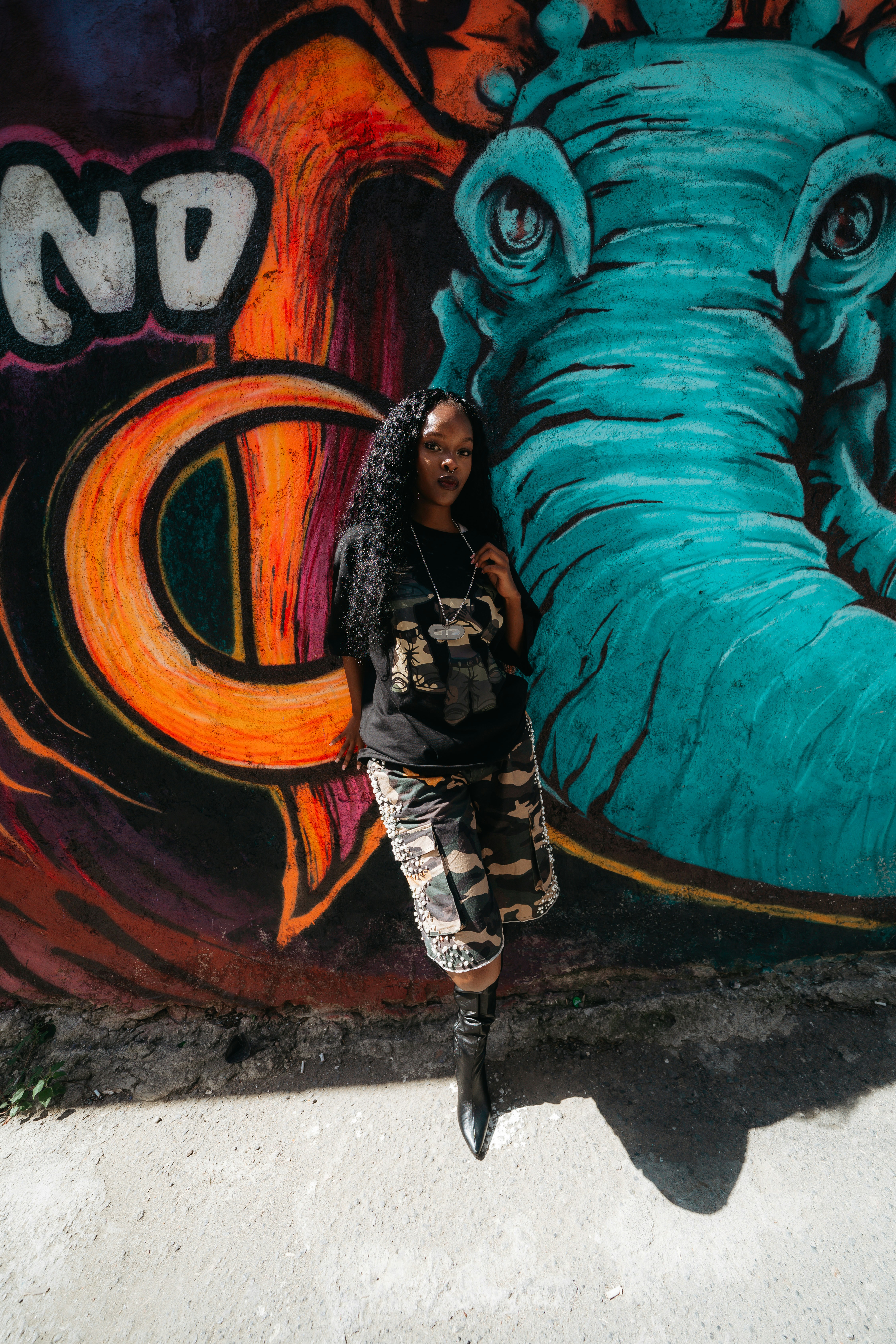 Graffiti Muse: A Woman Posing Before a Vivid Elephant Mosaic
