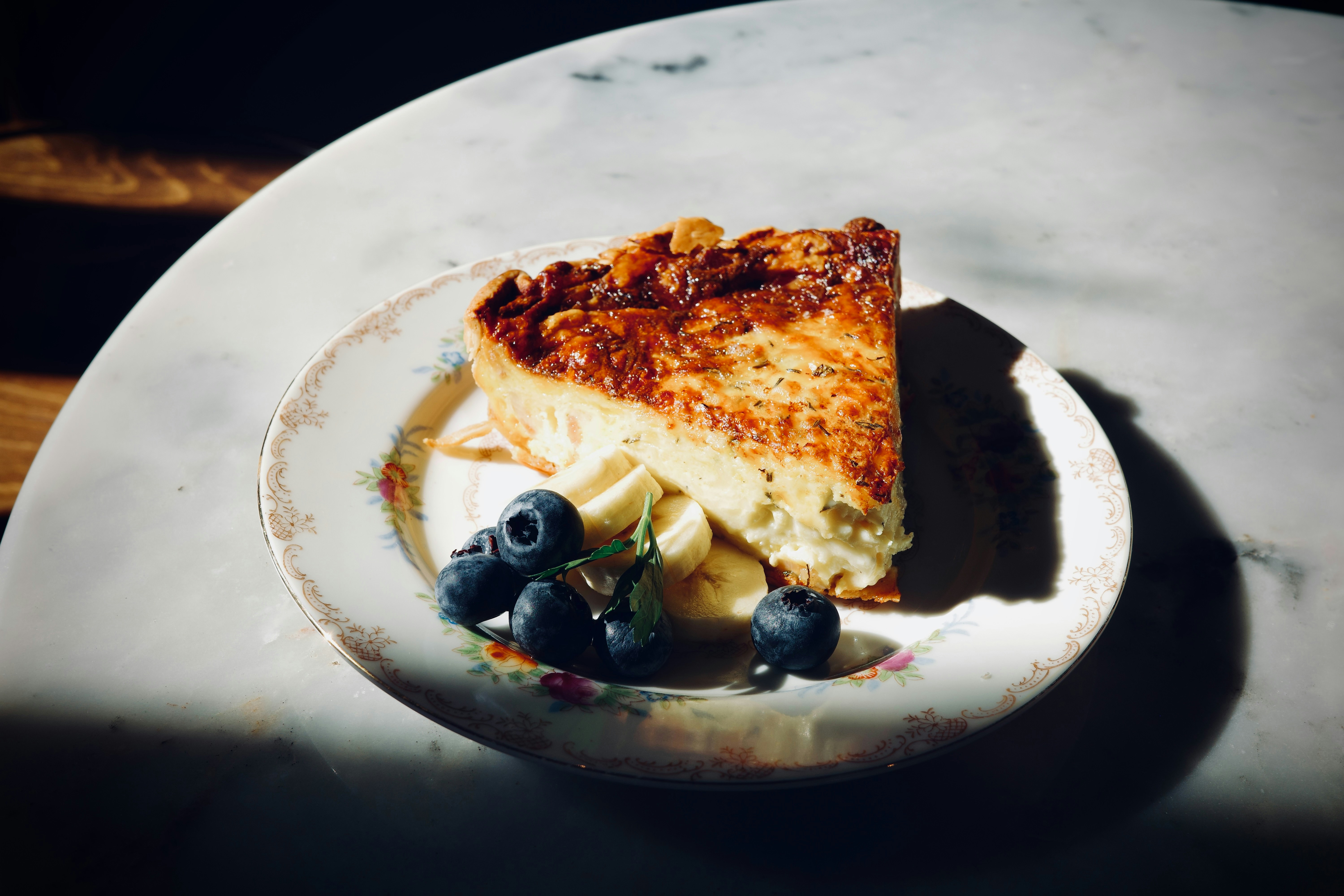 Sunlit Slice: Creamy Cheesecake with Blueberry Crown on a Marble Table