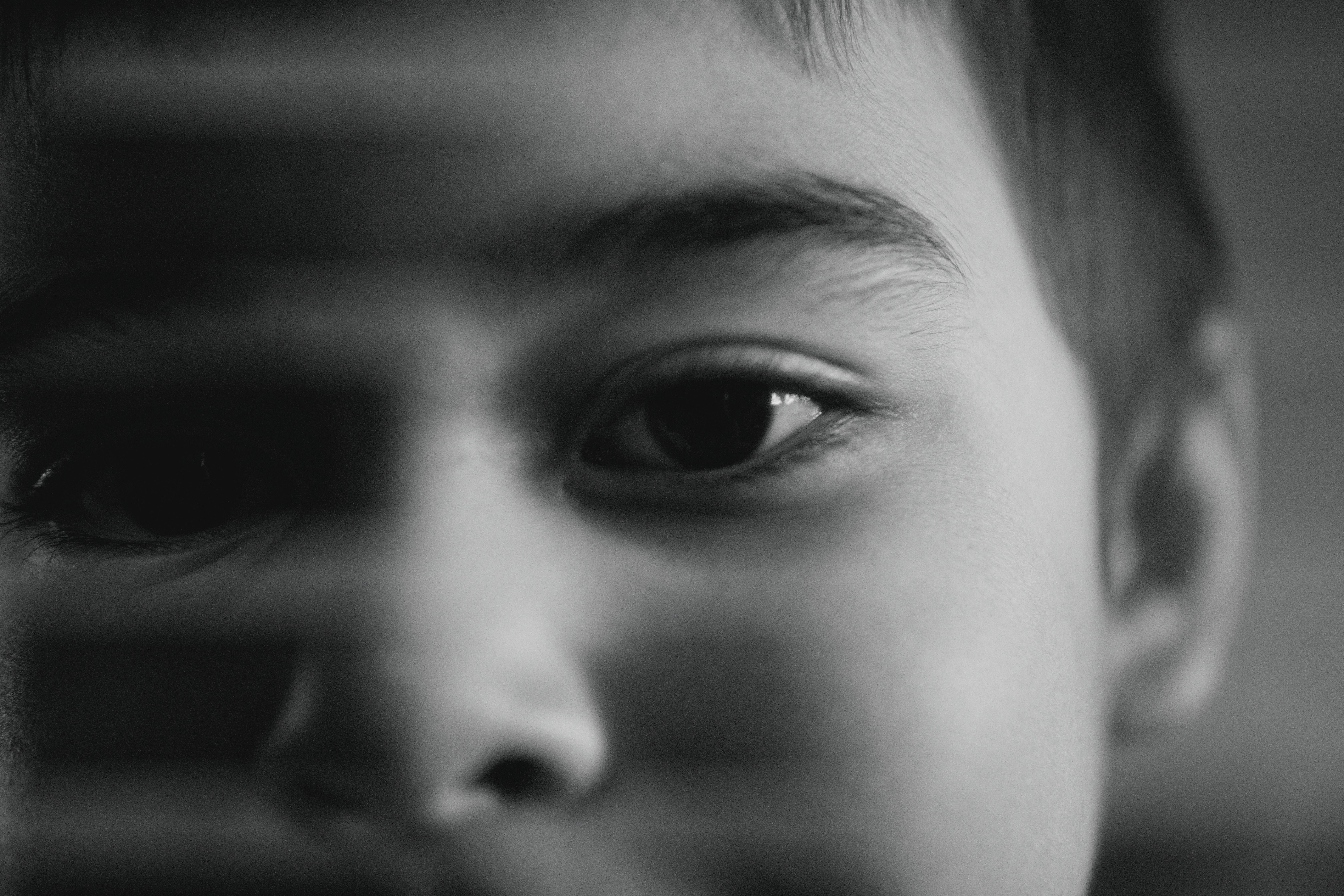 Close-up of a young face with horizontal bands across the frame, emphasizing the eye and partial nose region. The monochrome portrait highlights texture and expression; the composition centers the viewer on the subject’s eye through a narrow crop.