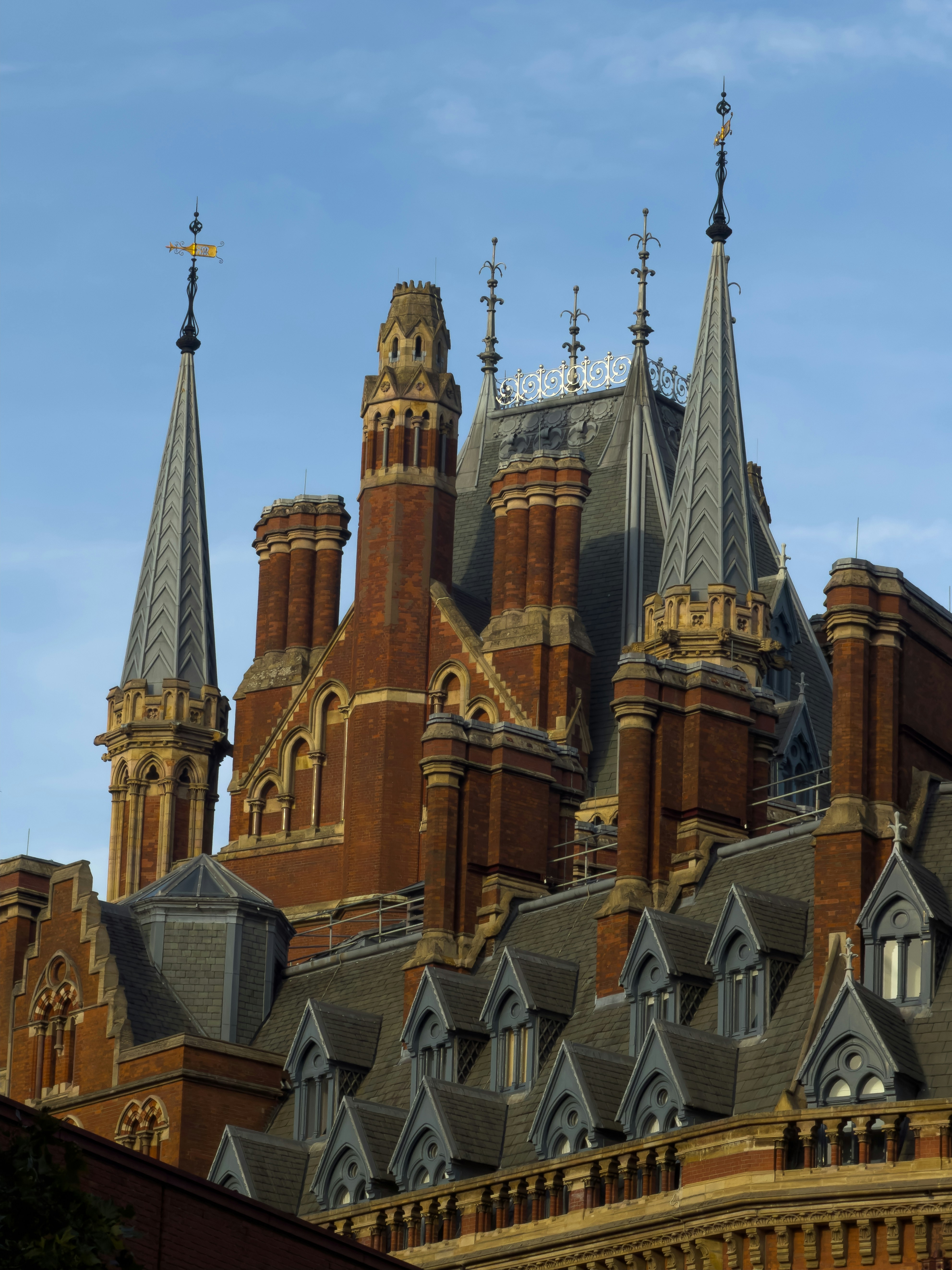 Ornate brick Gothic roofline with multiple spires and chimneys against a clear blue sky.