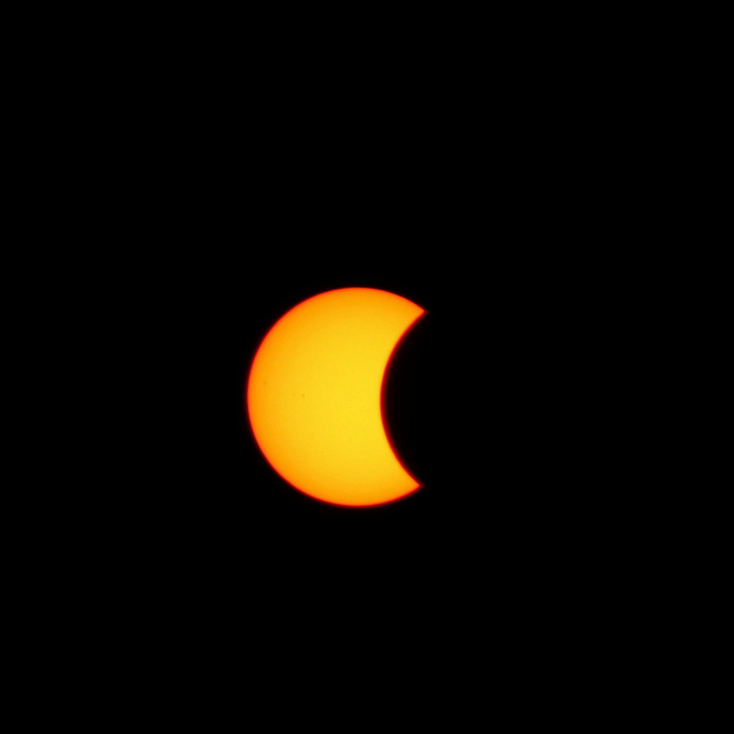 Une photographie astronomique saisissante d'une éclipse solaire partielle, mettant en scène un disque solaire transformé en un vibrant croissant orange vif. Se détachant de manière minimaliste sur un fond noir absolu, le soleil semble grignoté par l'ombre parfaitement nette de la Lune. Cette image cosmique et épurée met en valeur la beauté géométrique des alignements célestes. Un visuel idéal pour illustrer des projets liés à l'astronomie, à la science, aux événements spatiaux ou à la photographie d'art minimaliste.