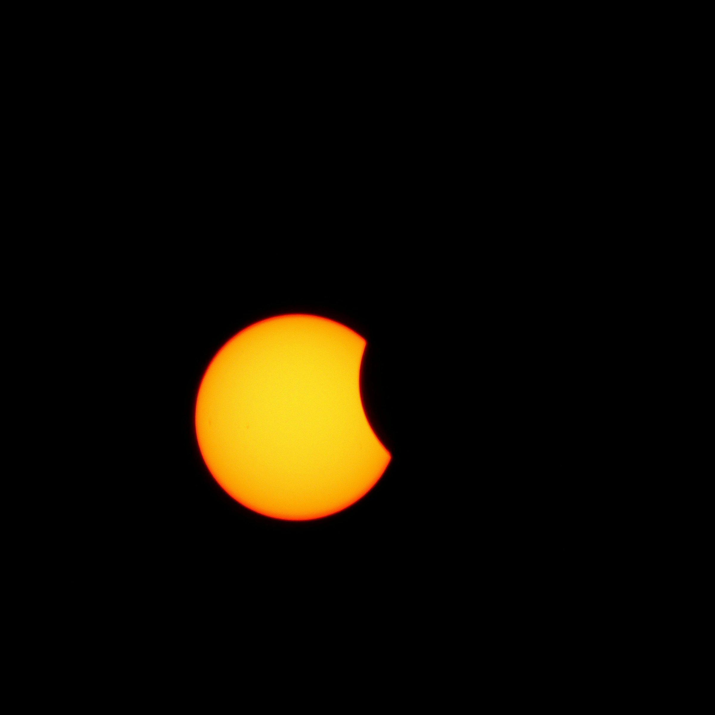 Une photographie astronomique saisissante d'une éclipse solaire partielle, mettant en scène un disque solaire transformé en un vibrant croissant orange vif. Se détachant de manière minimaliste sur un fond noir absolu, le soleil semble grignoté par l'ombre parfaitement nette de la Lune. Cette image cosmique et épurée met en valeur la beauté géométrique des alignements célestes. Un visuel idéal pour illustrer des projets liés à l'astronomie, à la science, aux événements spatiaux ou à la photographie d'art minimaliste