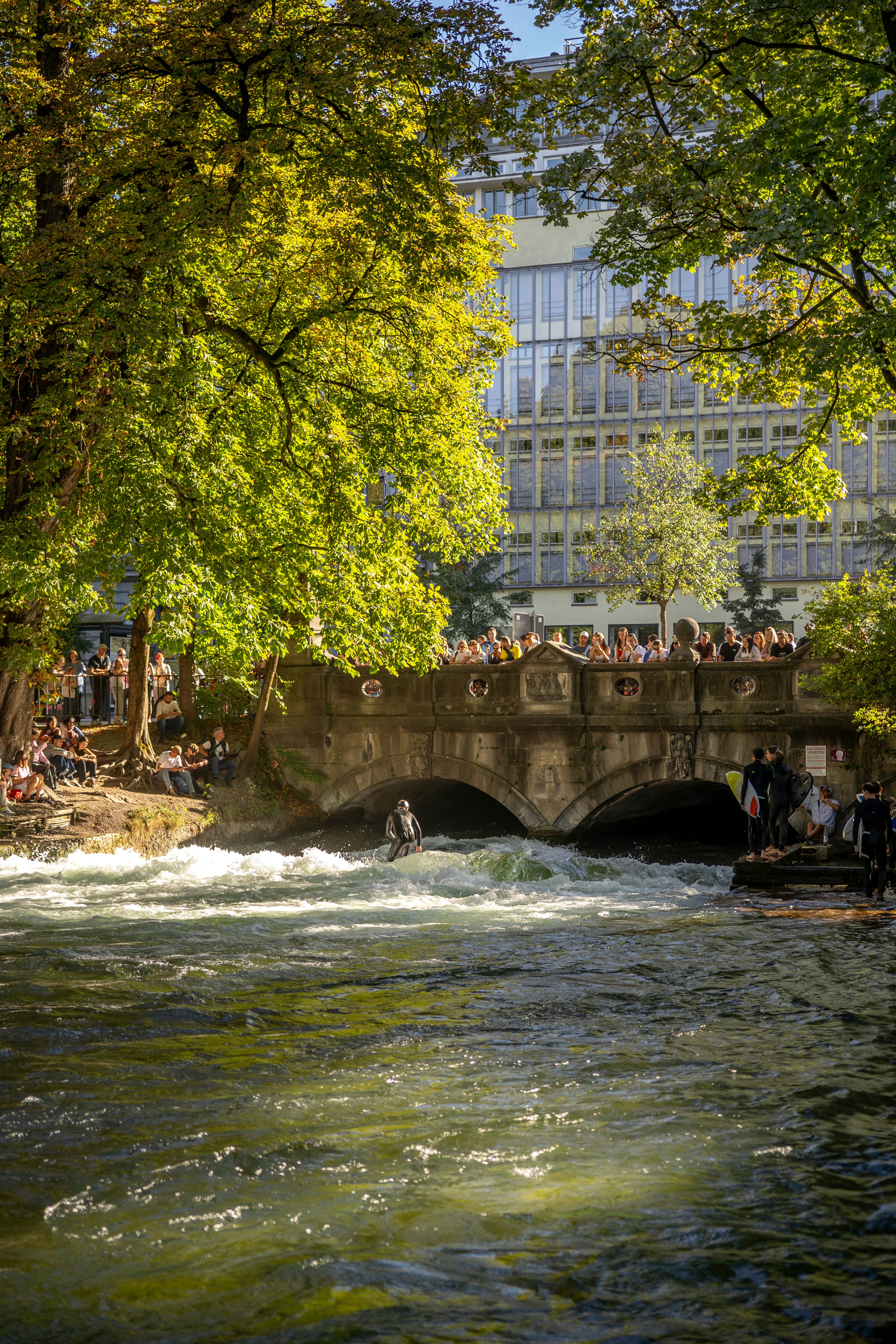 Crowd on the Stone Bridge Over a Swift River Framed by Sunlit Foliage
