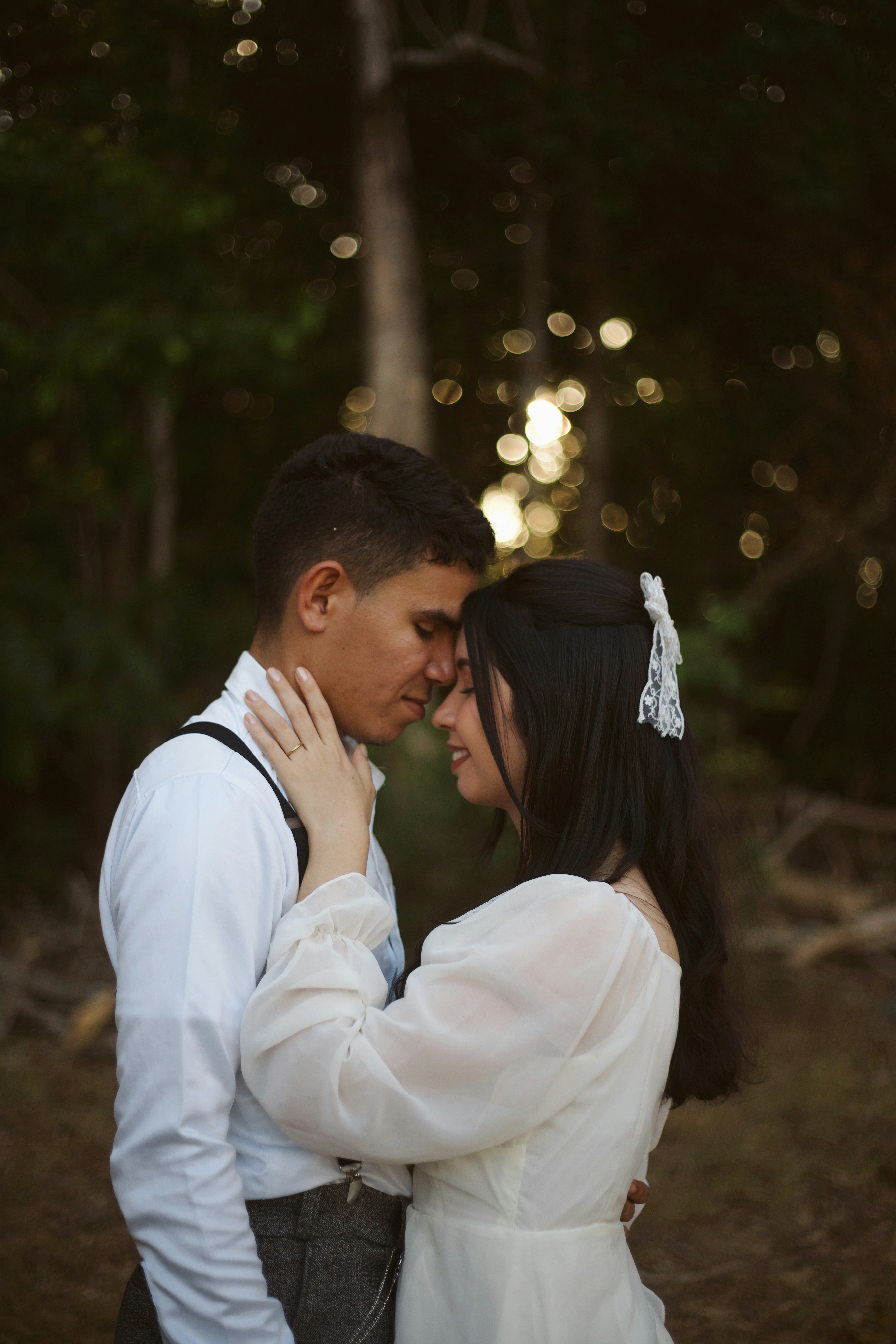 A man and a woman with foreheads touching in a forest with bokeh light