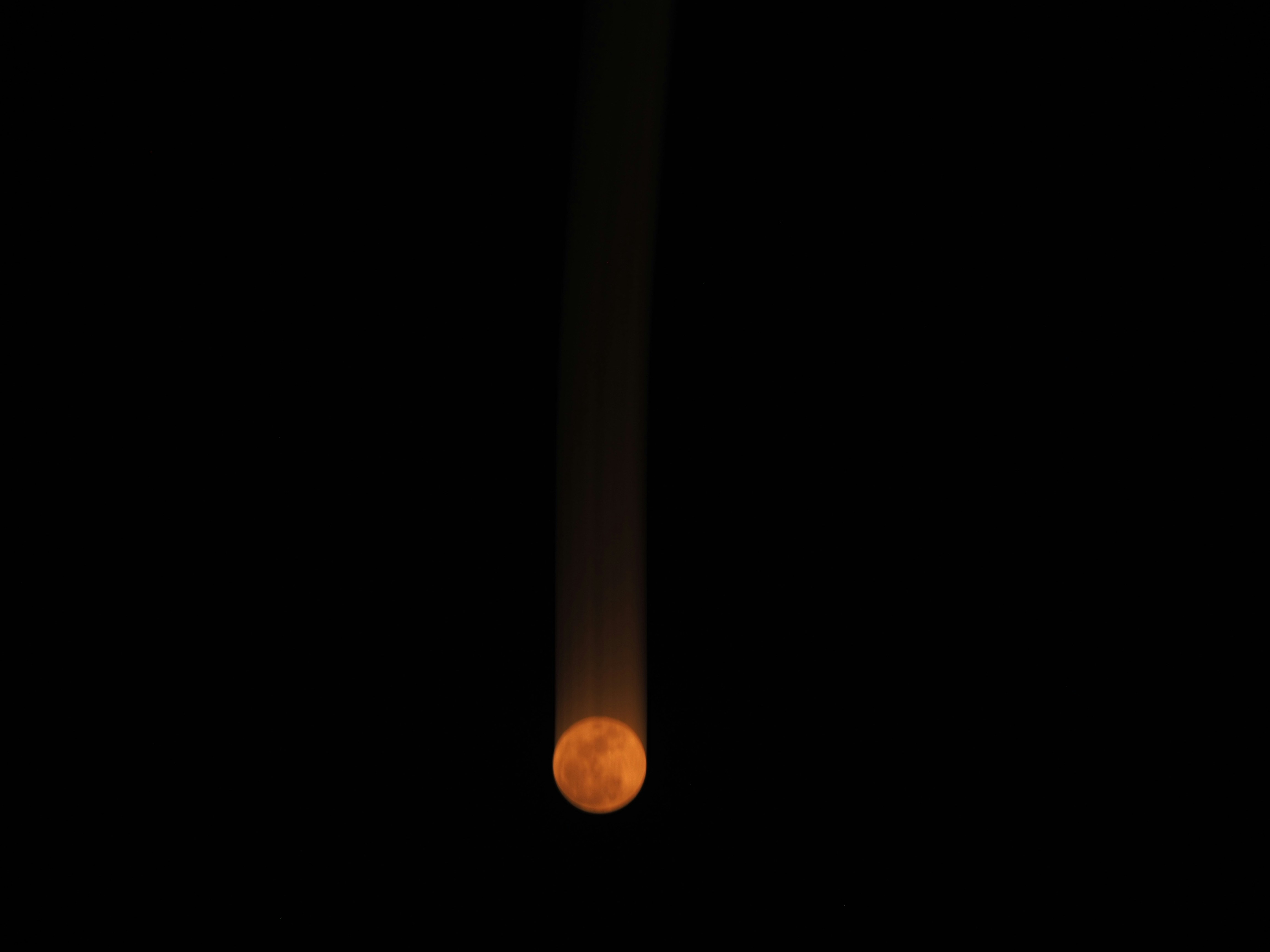 A long exposure of an orange moon leaving a vertical light trail