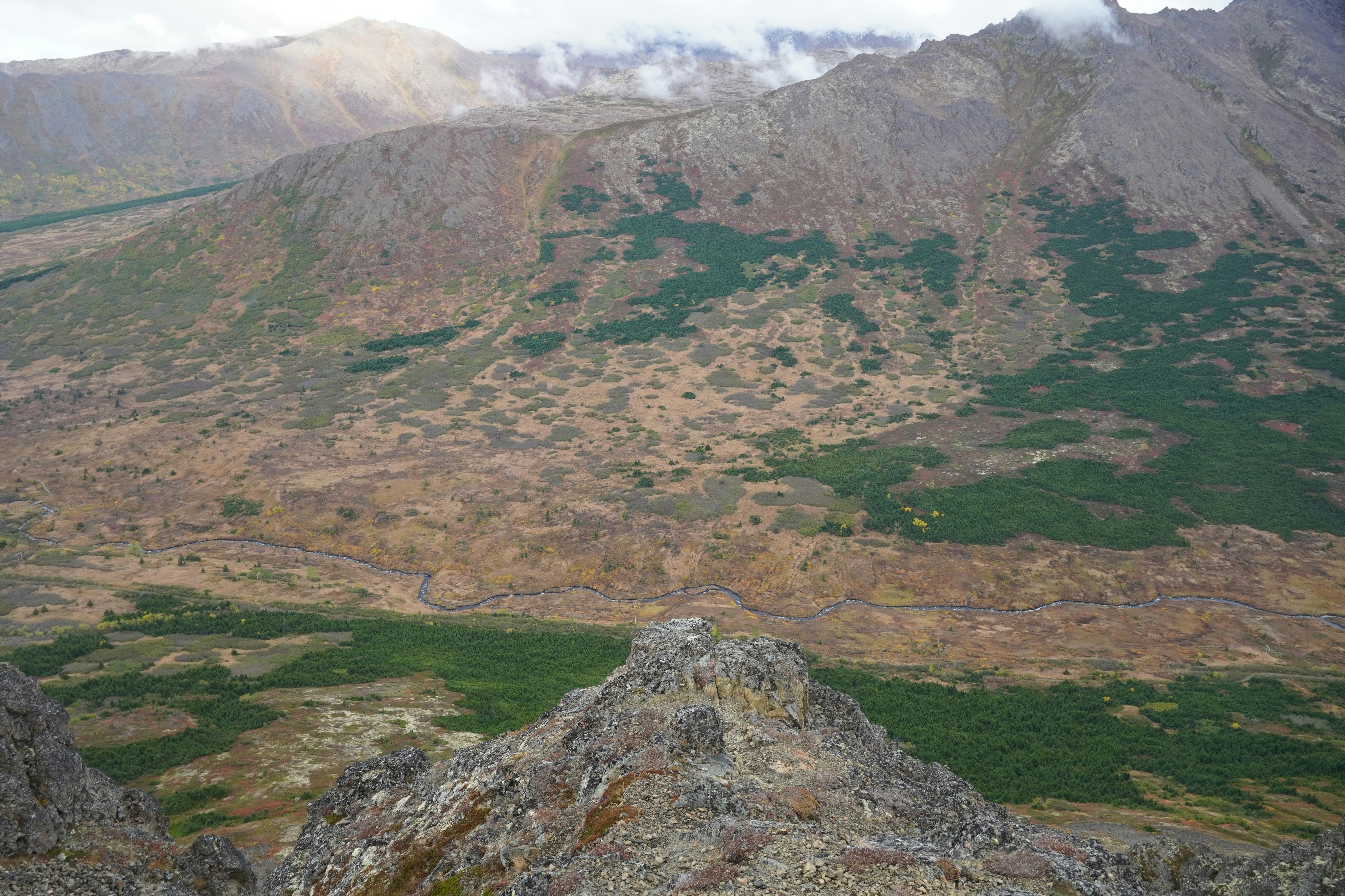 A winding stream through a vast valley below rugged mountain slopes