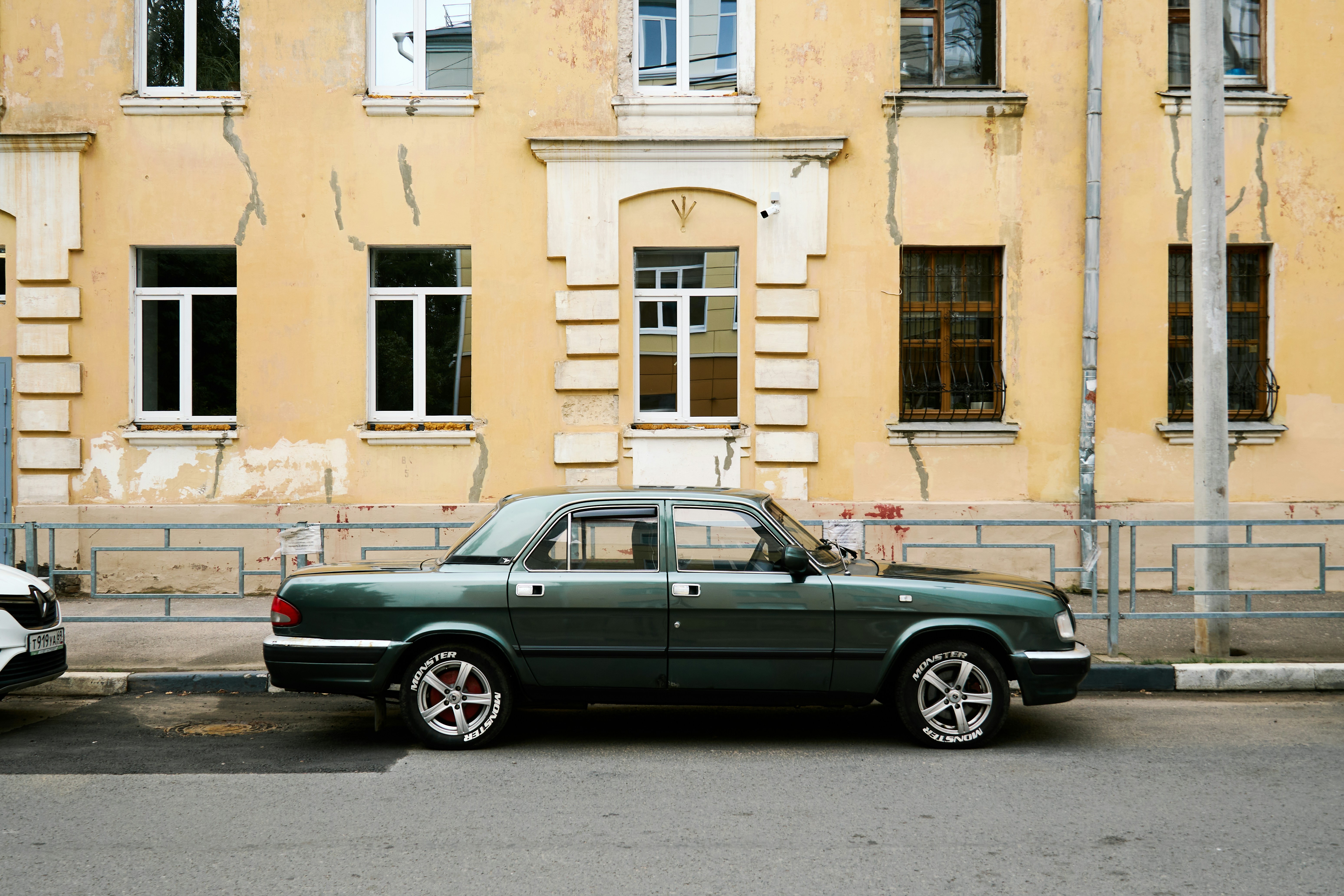 Green sedan in front of a sunlit yellow-brick building with peeling plaster