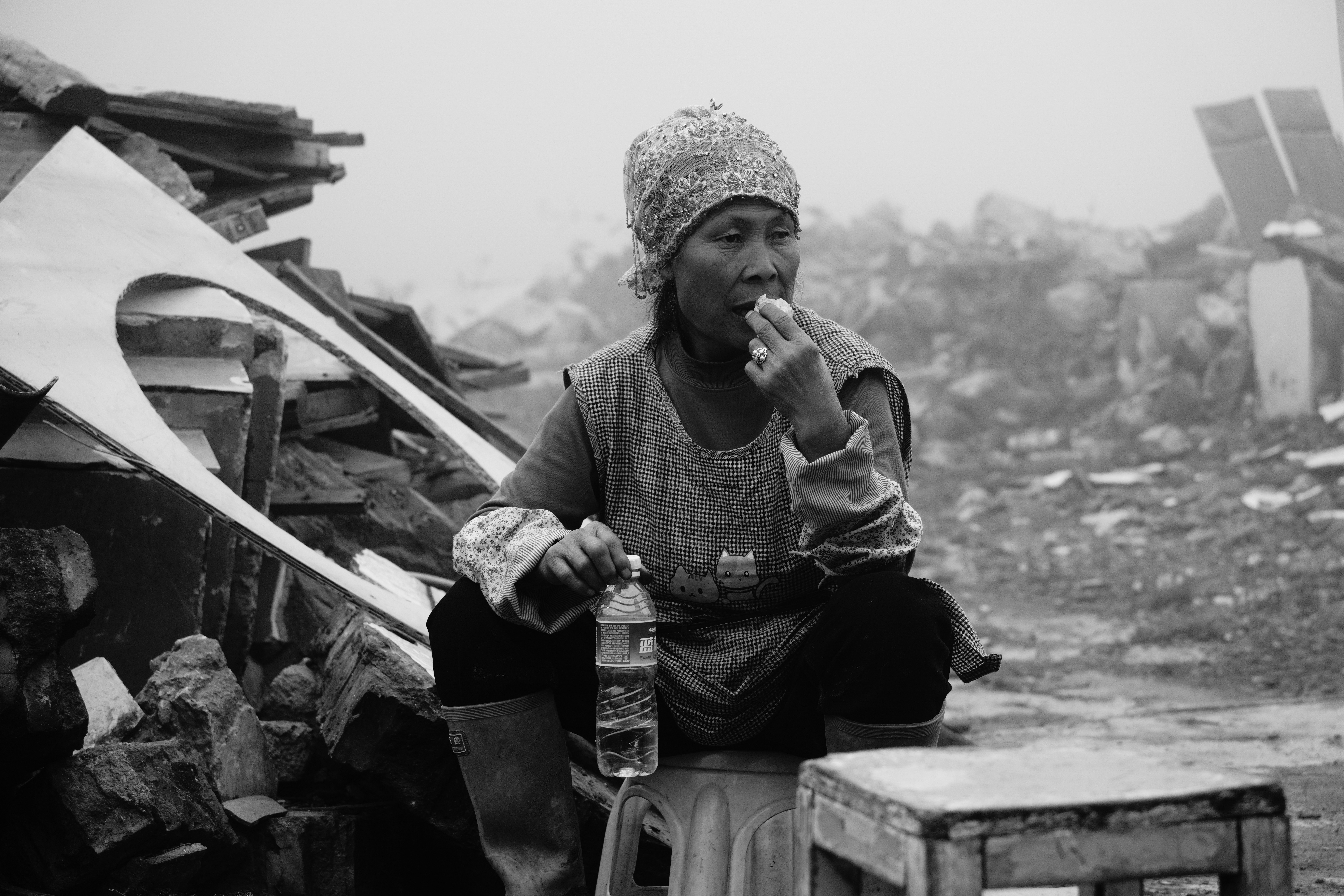 Woman in a rubble-strewn landscape pauses with water bottle and snack