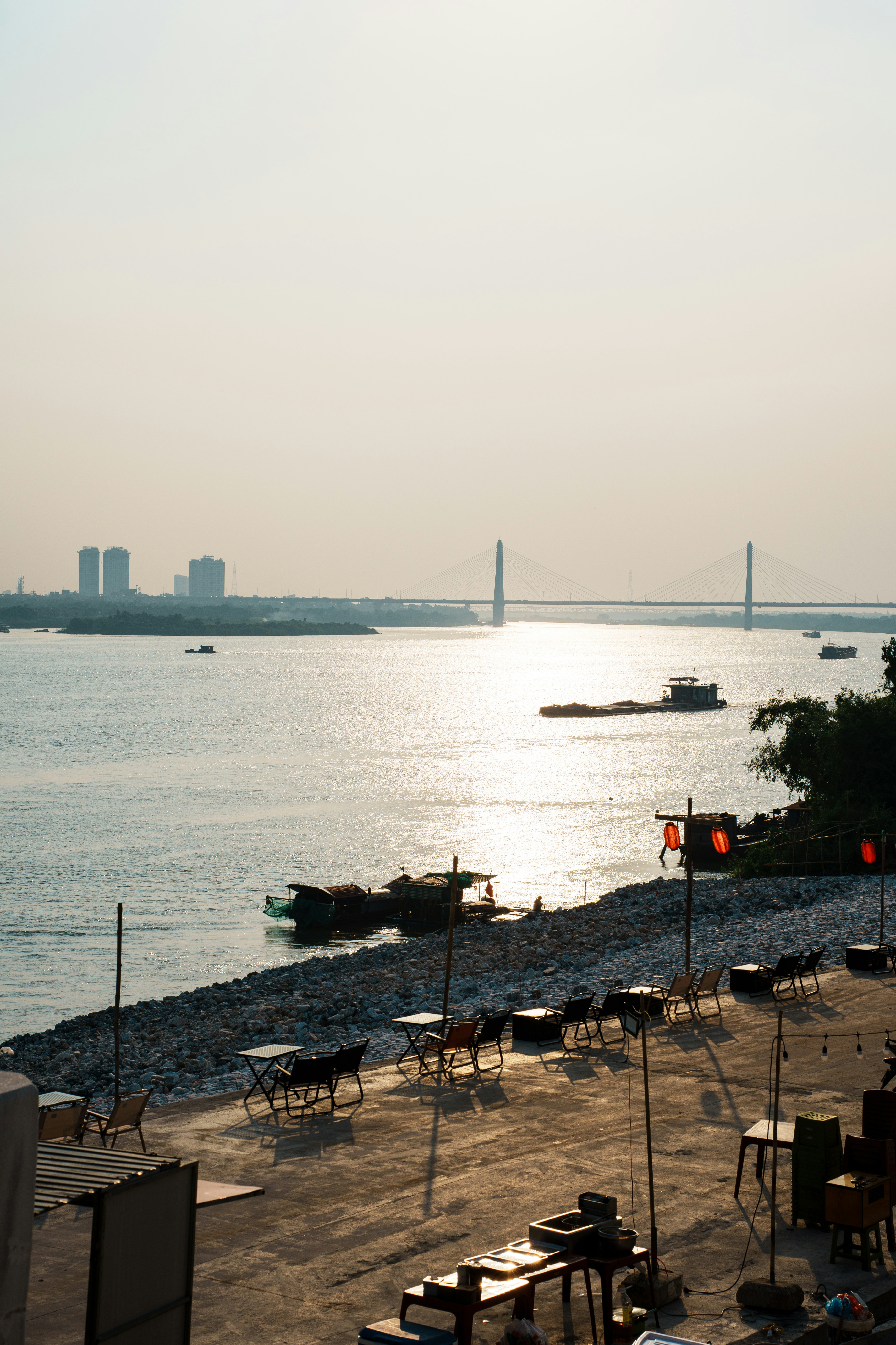Sunlit Riverside Calm: Boats, Lanterns, and a Distant Bridge