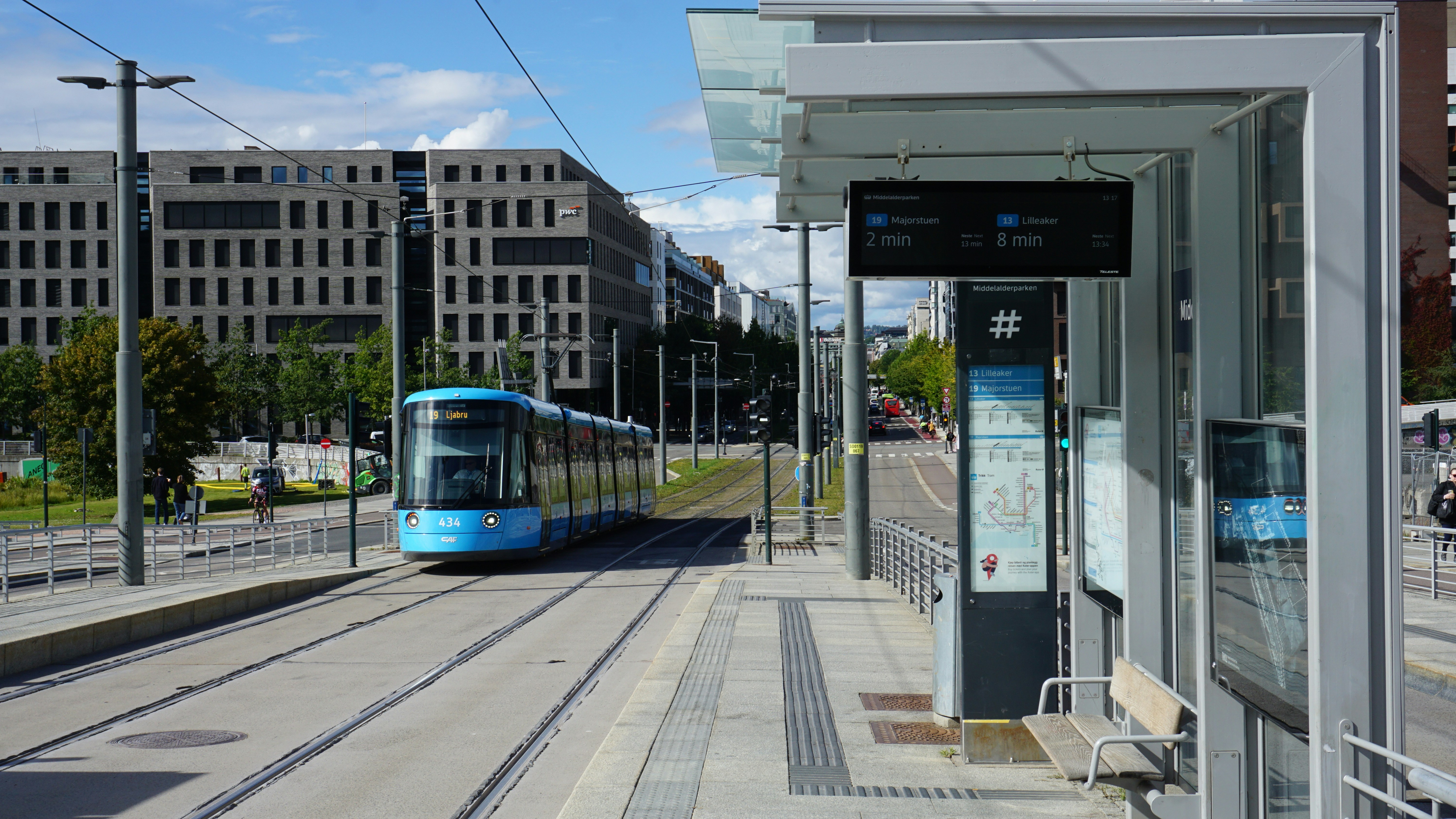 Blue tram glides toward a modern city tram stop under a bright sky