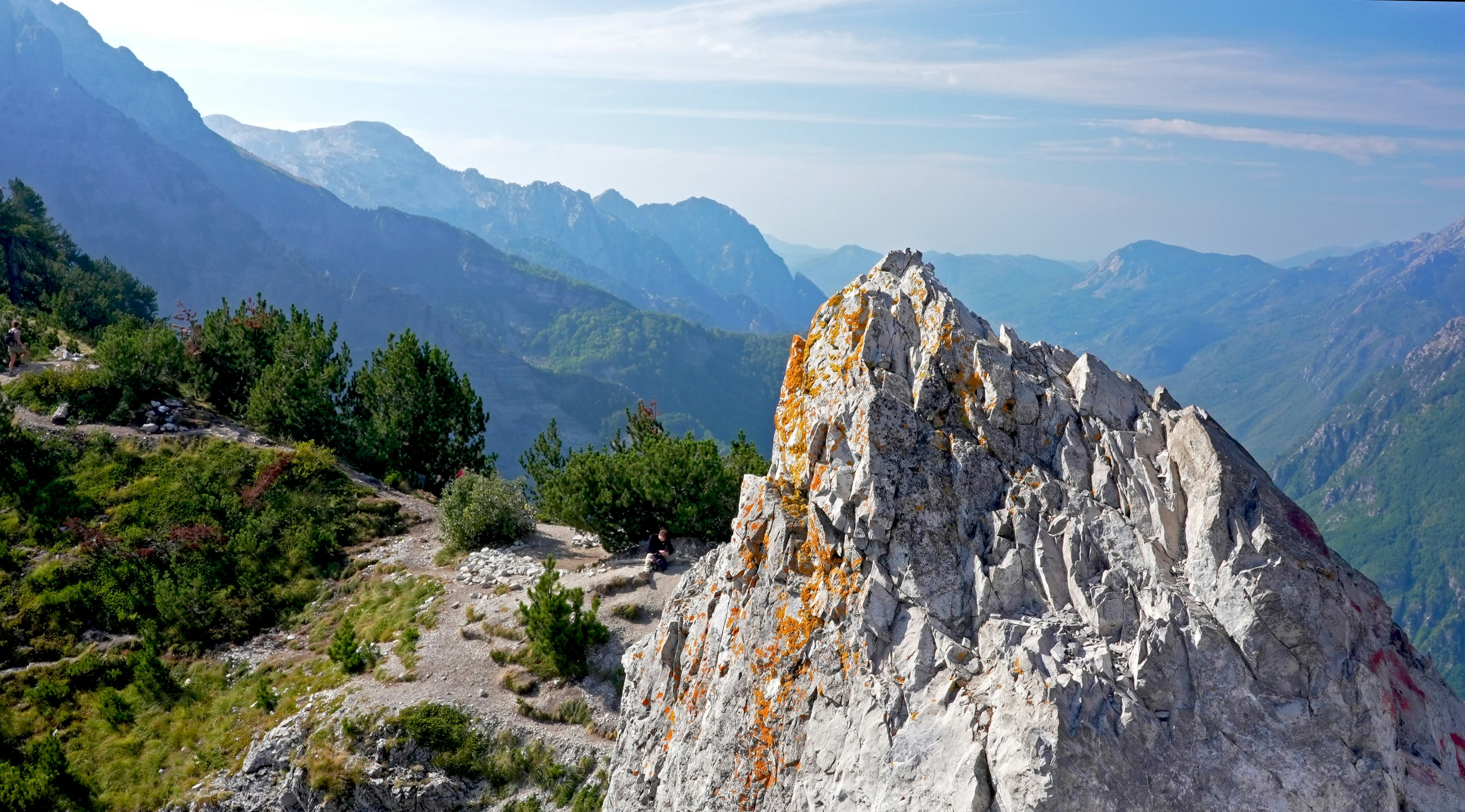 Jagged granite outcrop in the foreground with a sweeping valley and distant ridgelines under a clear blue sky.