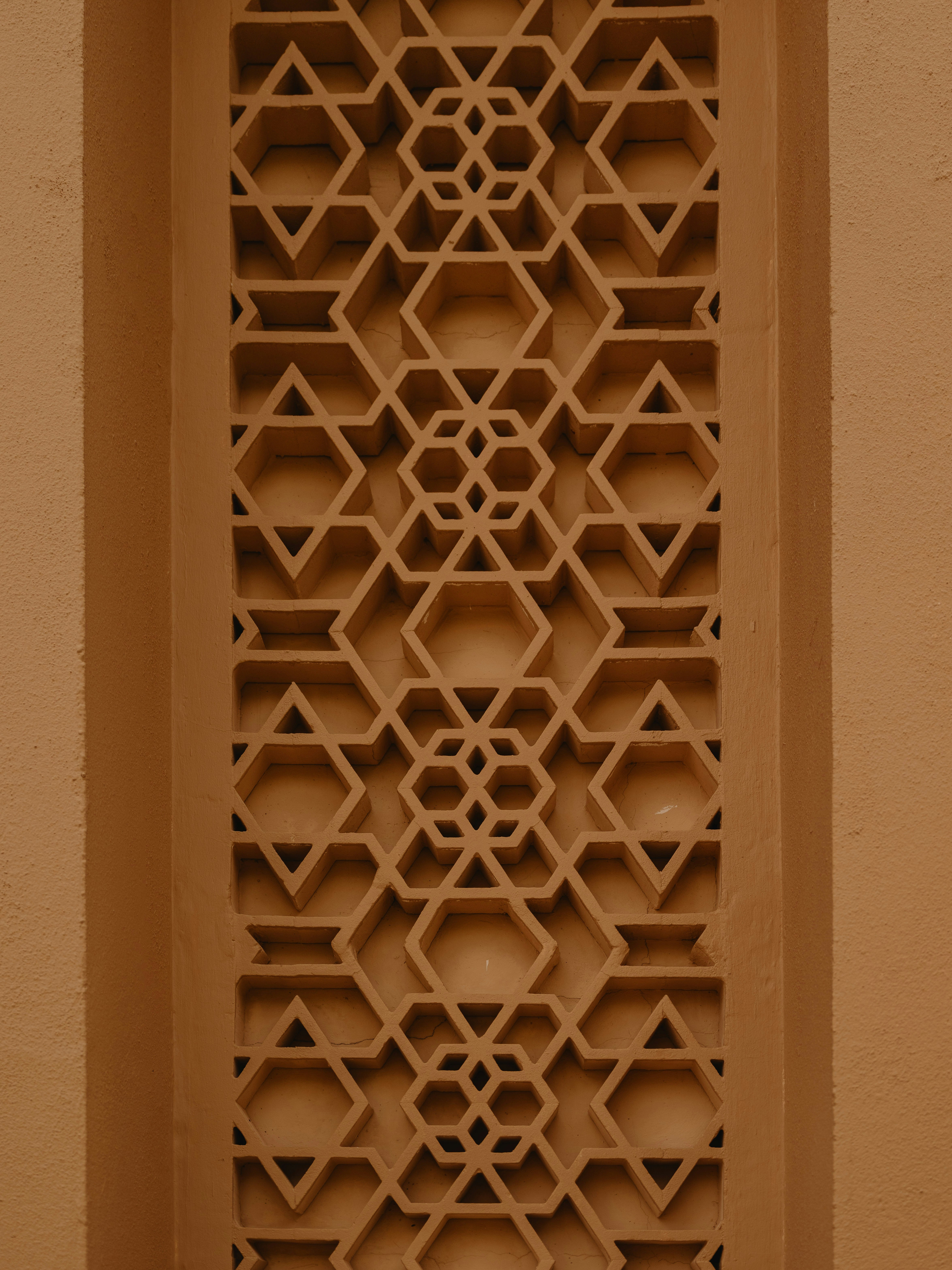 Close up of a carved geometric lattice screen at Masjid Tengku Ampuan in Kuala Lumpur, showing classic Islamic star patterns in warm sandstone.