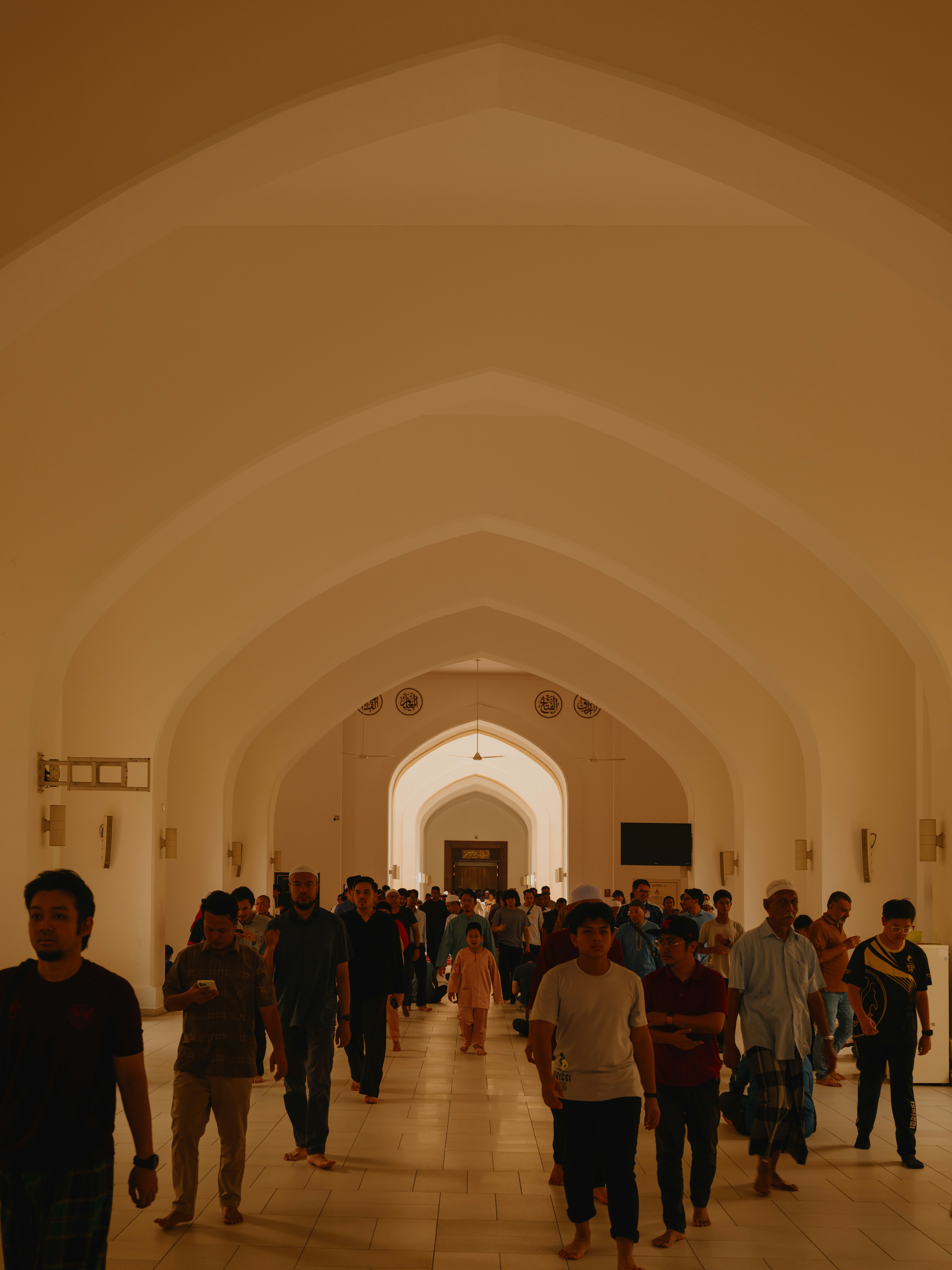 Worshippers walk through the long arched corridor of Masjid Tengku Ampuan in Kuala Lumpur, with rows of arches leading the eye to the far door.