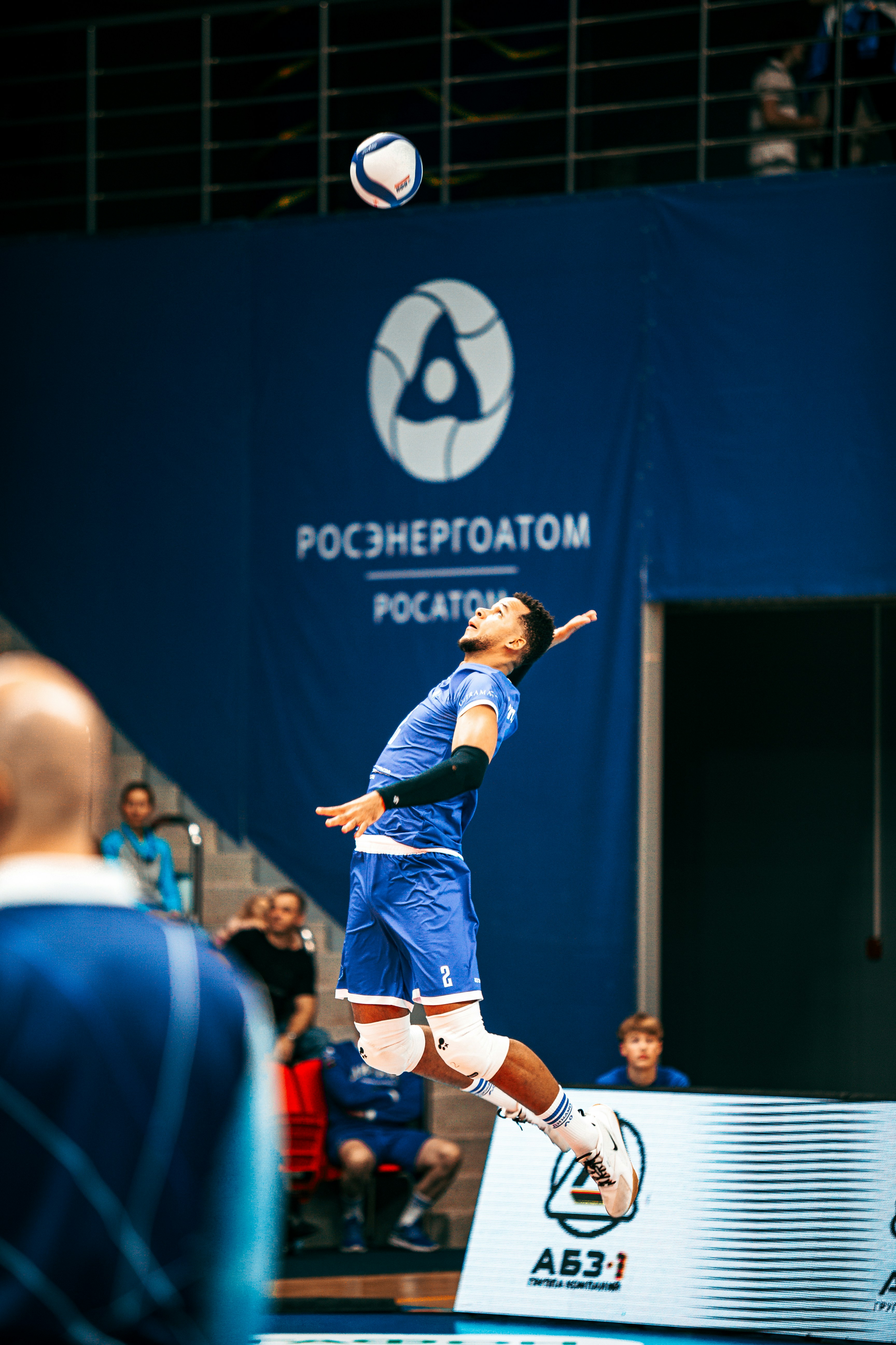 Mid-Air Volley: A Blue-clad Athlete Returns a Serve Beneath a Dark Arena Banner