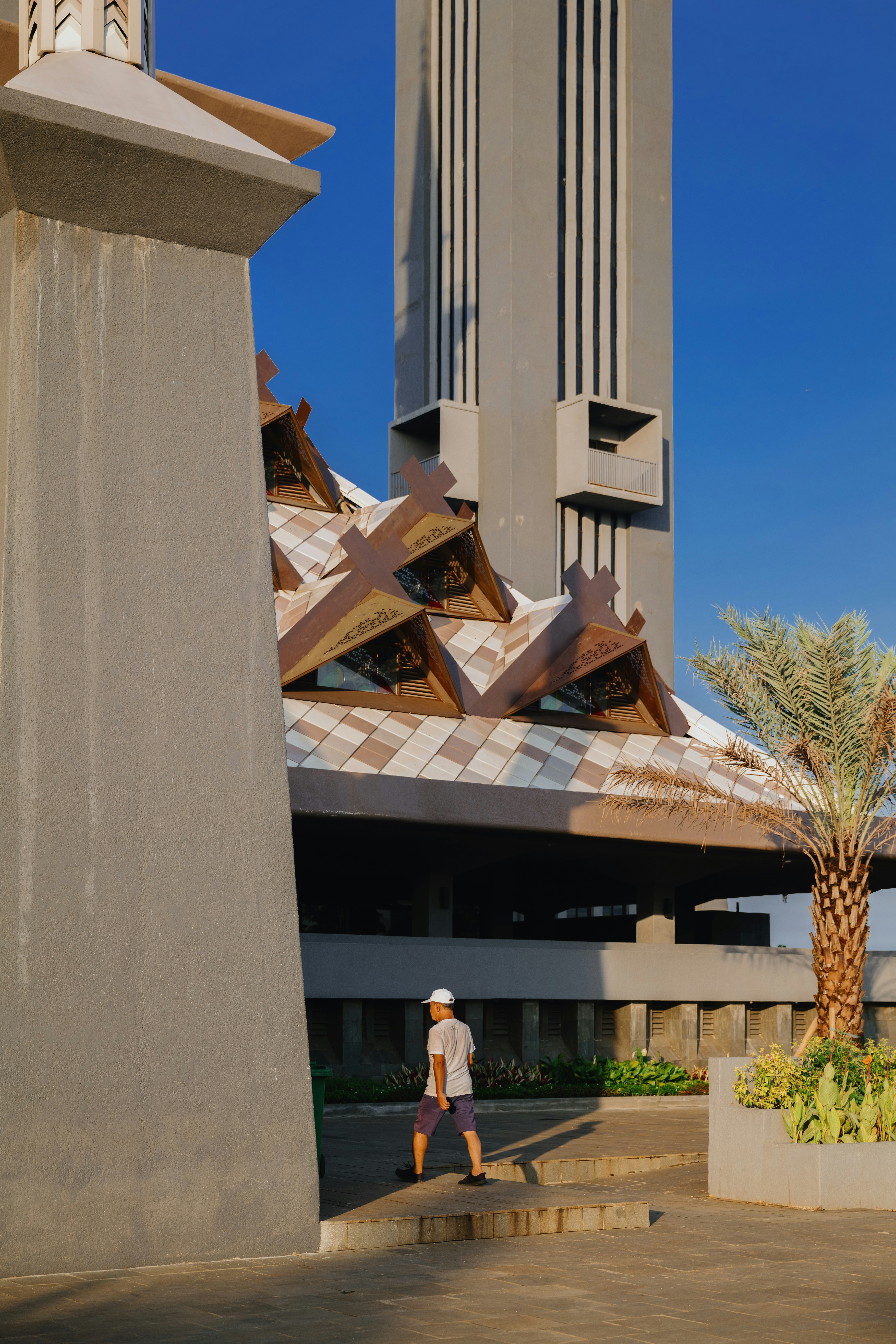 Footpath to the atrium: sunlit figure walks beneath a towering geometric facade