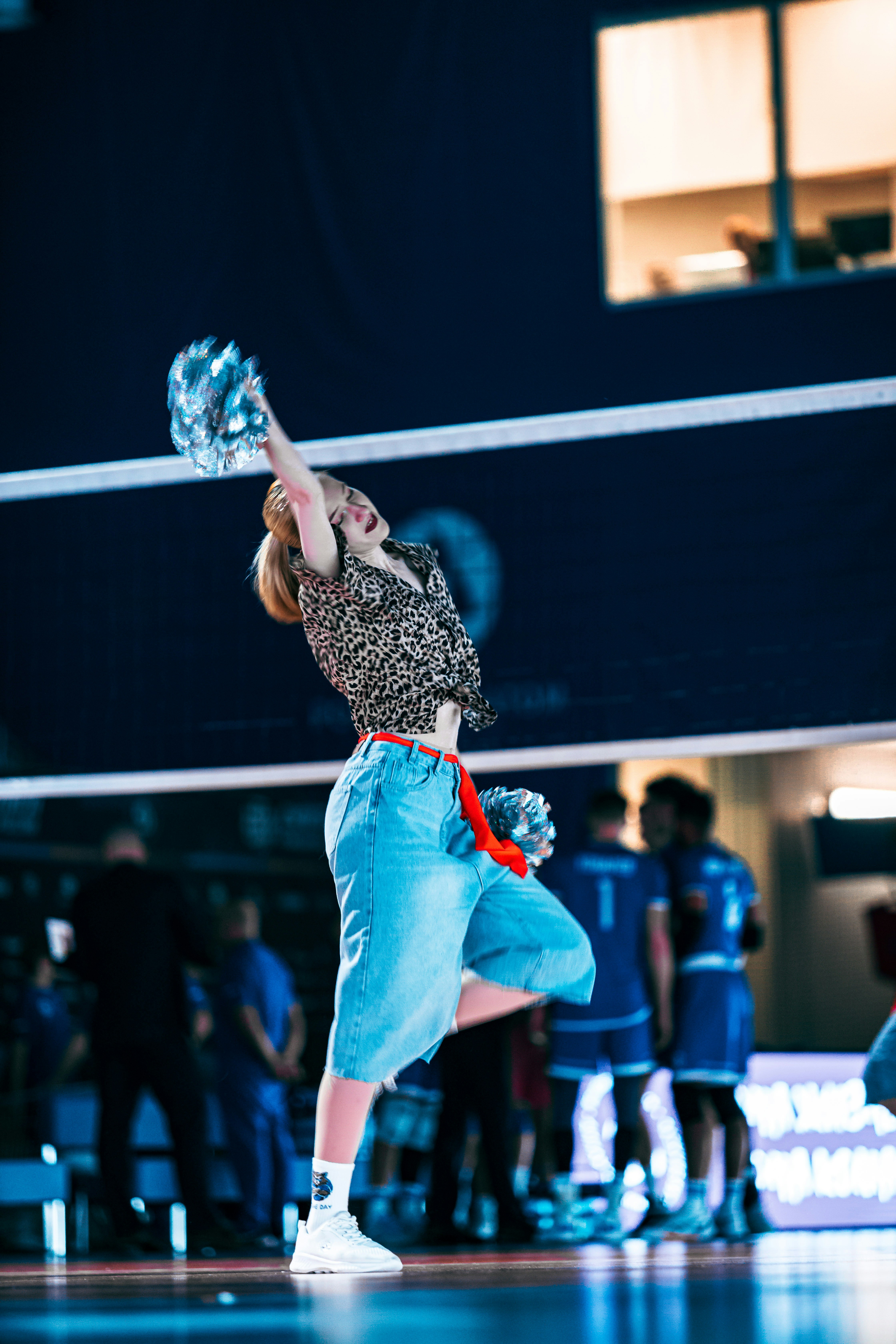 Midair Cheer: A Cheerleader Leaps with Metallic Pom-Poms Under Gym Lights
