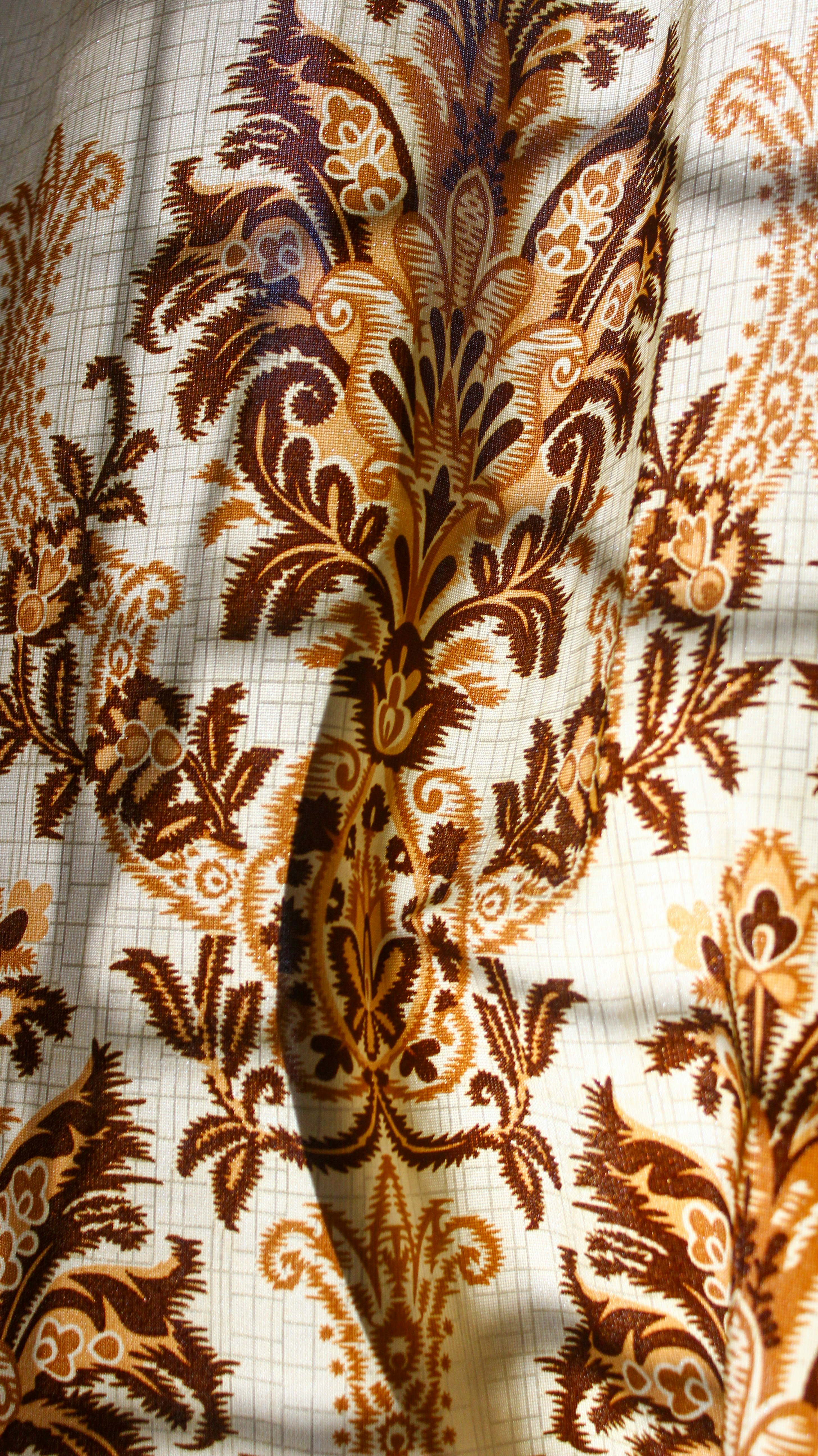 Close-up of ornate brown and gold damask fabric with a central seam and soft shadows, highlighting textile texture and pattern.