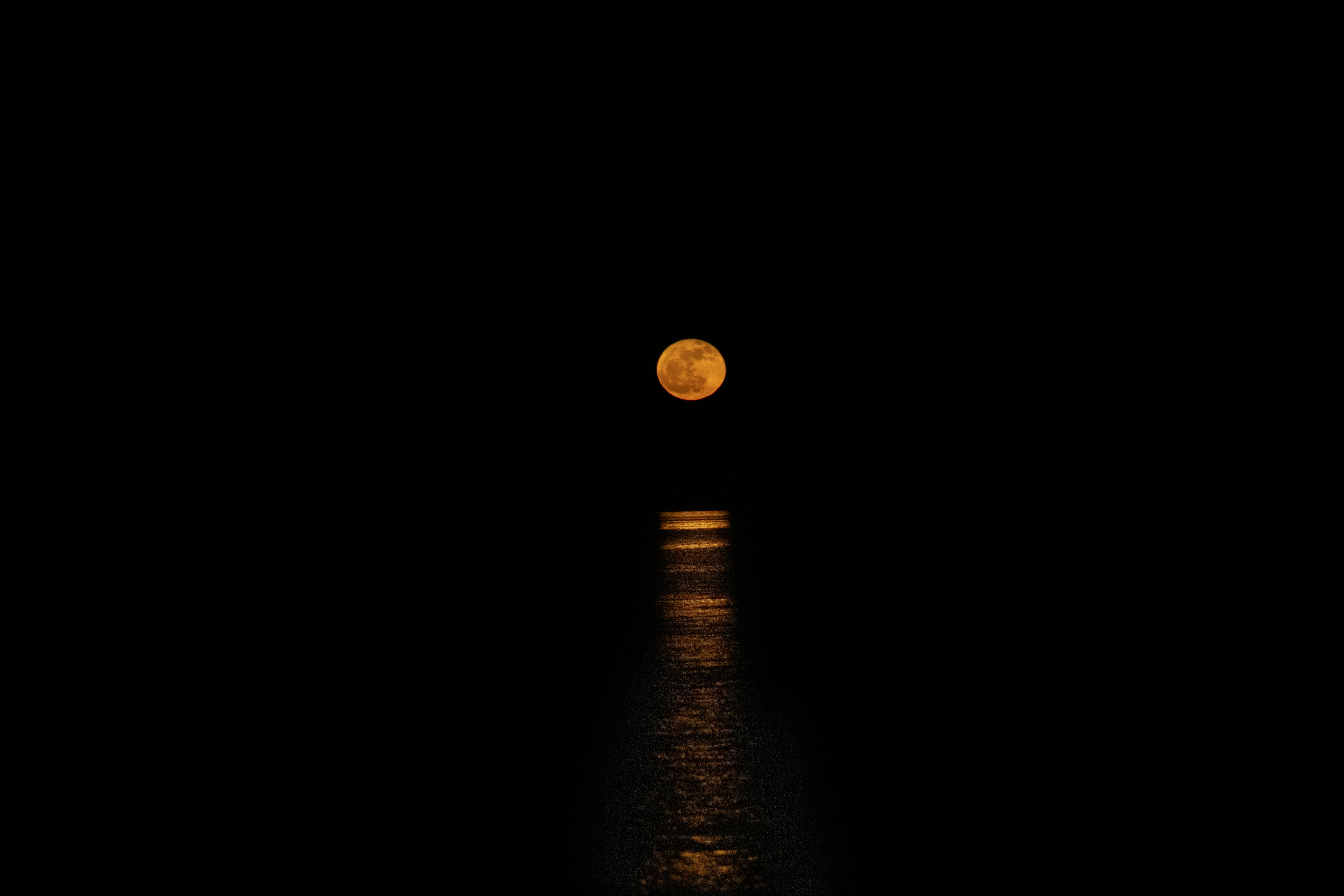 Moonrise over a silent sea: a lone orange orb on dark water