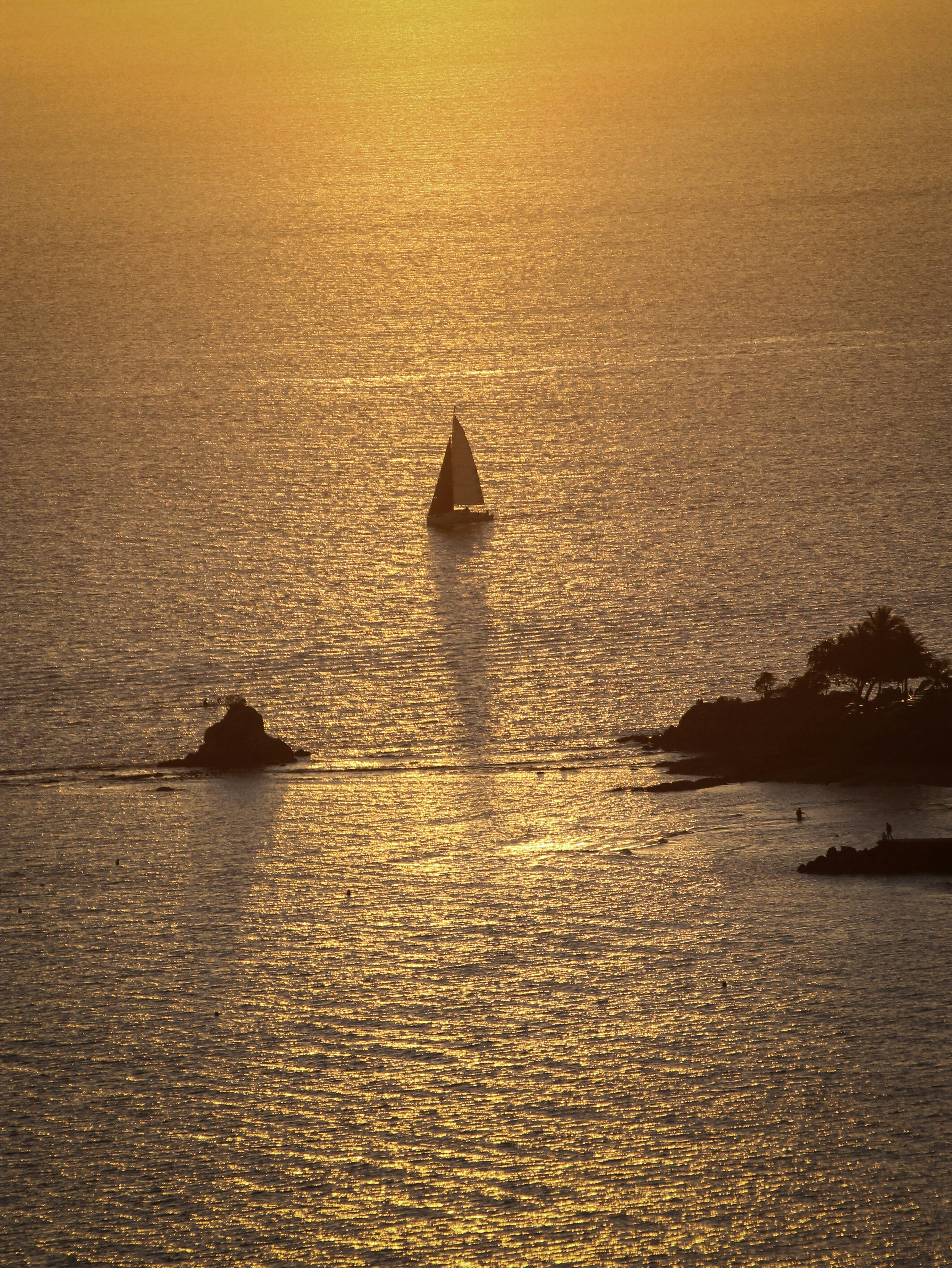 Golden Sail: A solitary sailboat drifting on molten sea at dusk