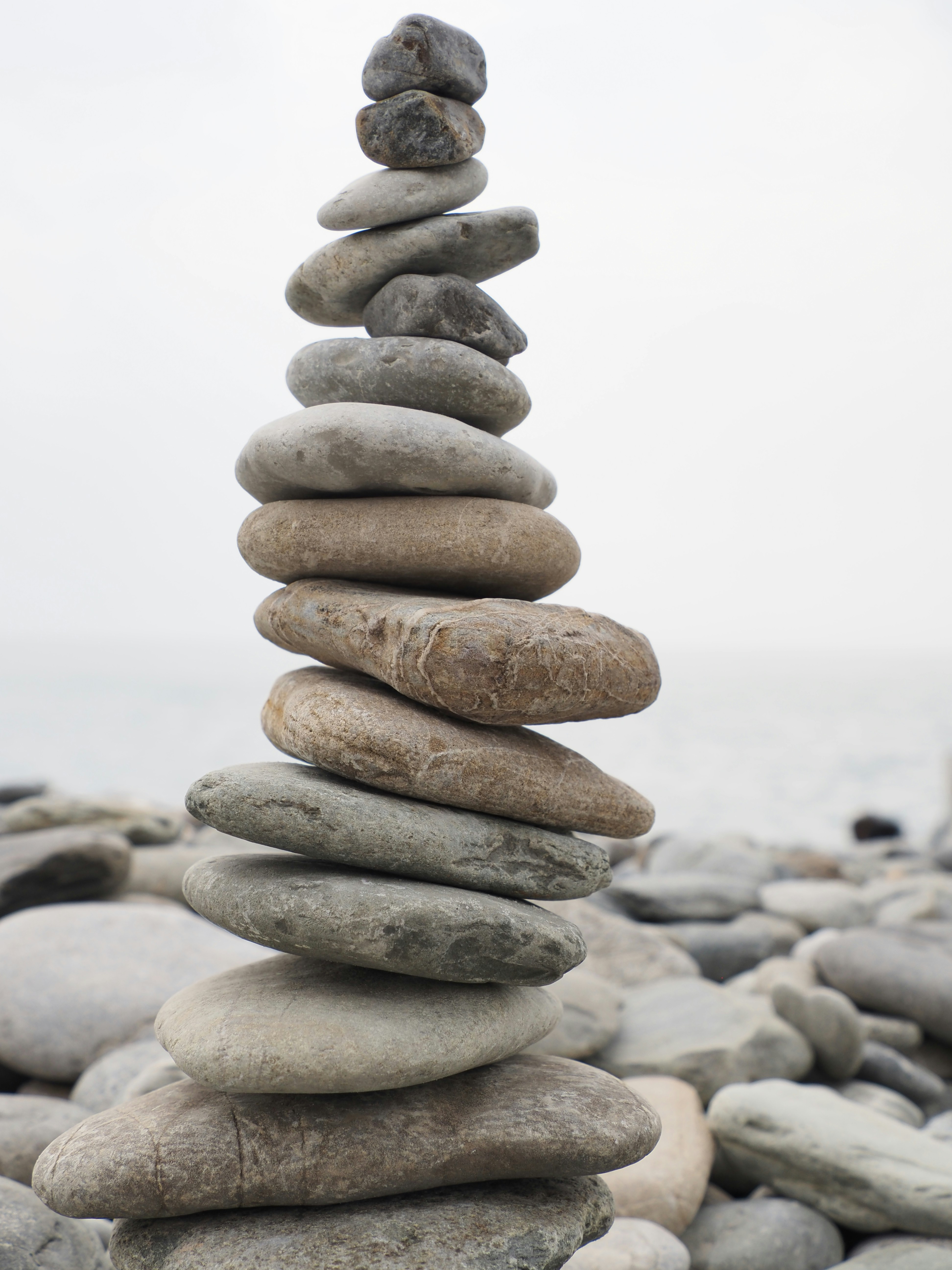 Pebble stack balanced along a rocky shore with a soft, overcast horizon in the background.