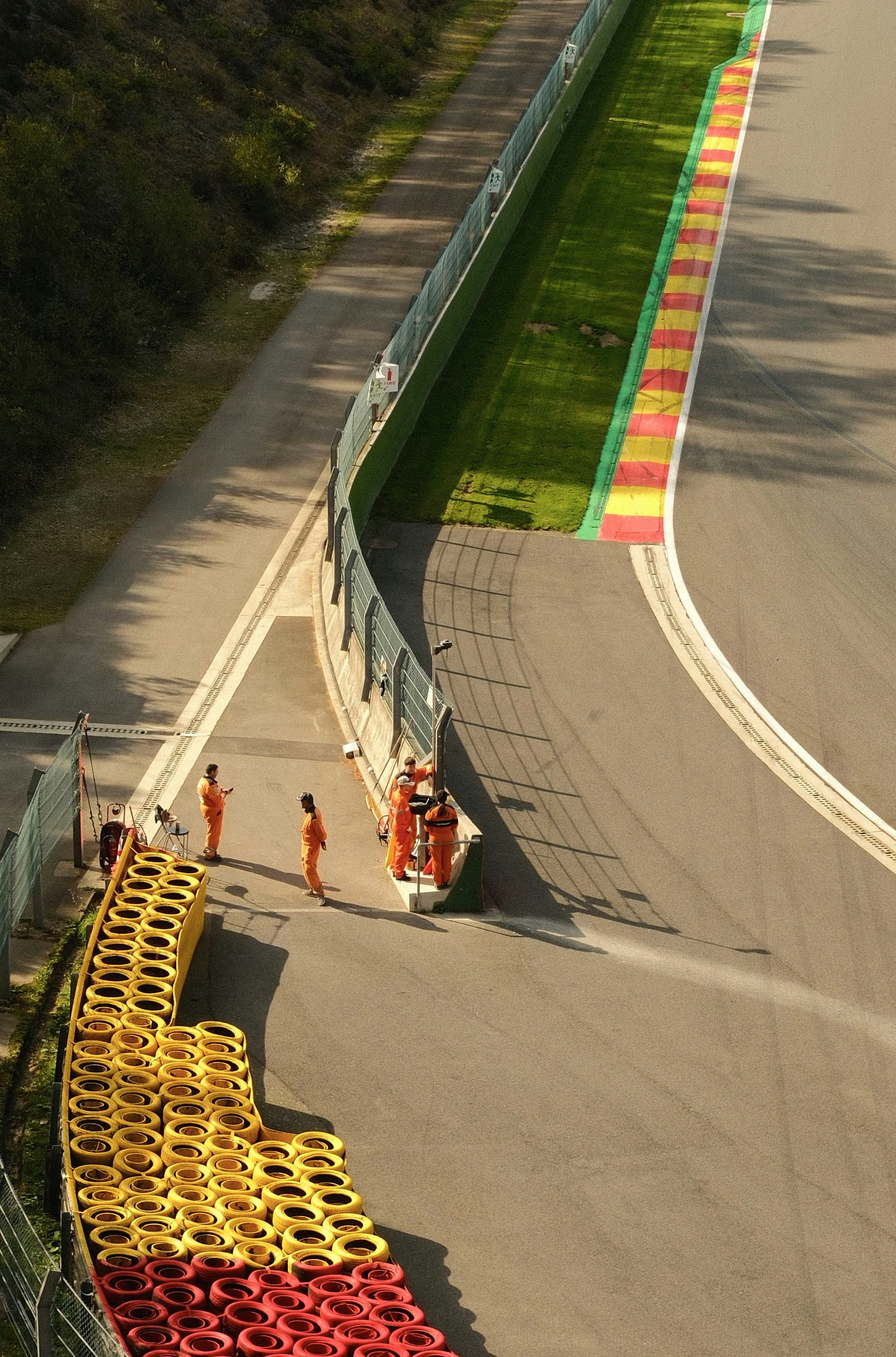 Orange-clad pit crew at the edge of sunlit raceway barriers