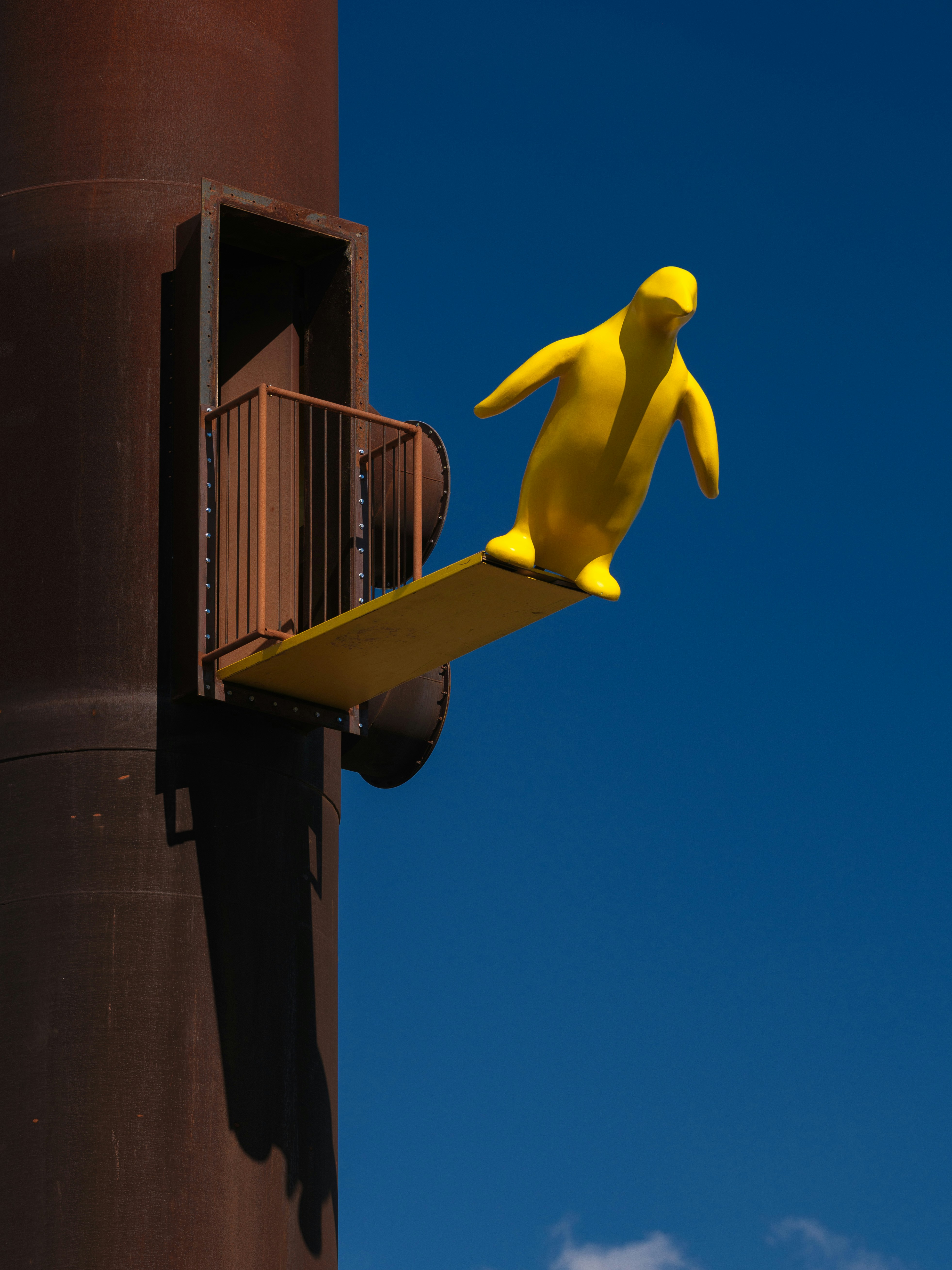Yellow Figure Balances on a Slanted Platform from a Rusty Tower