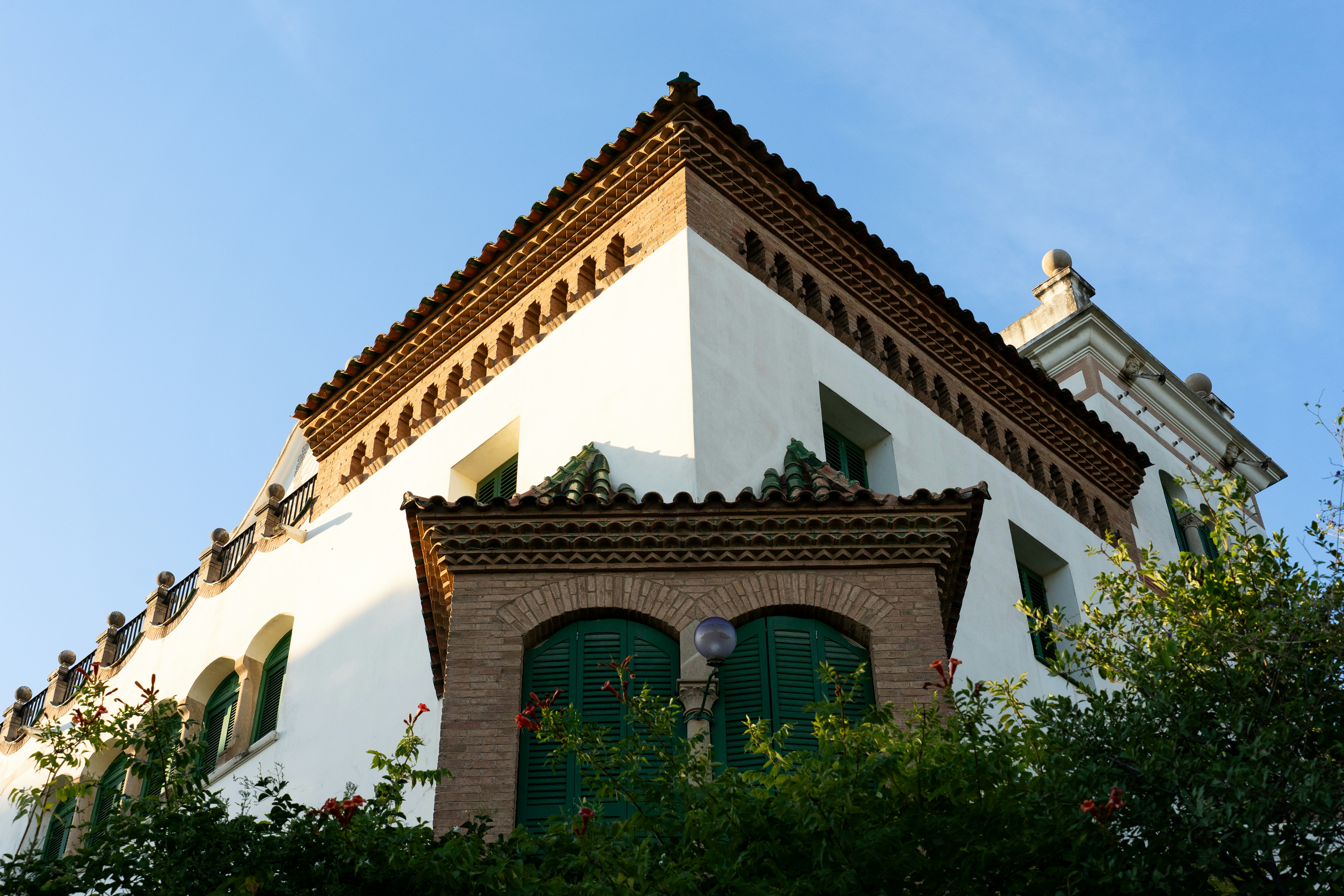 A white building with brick trim and green shutters under a clear blue sky