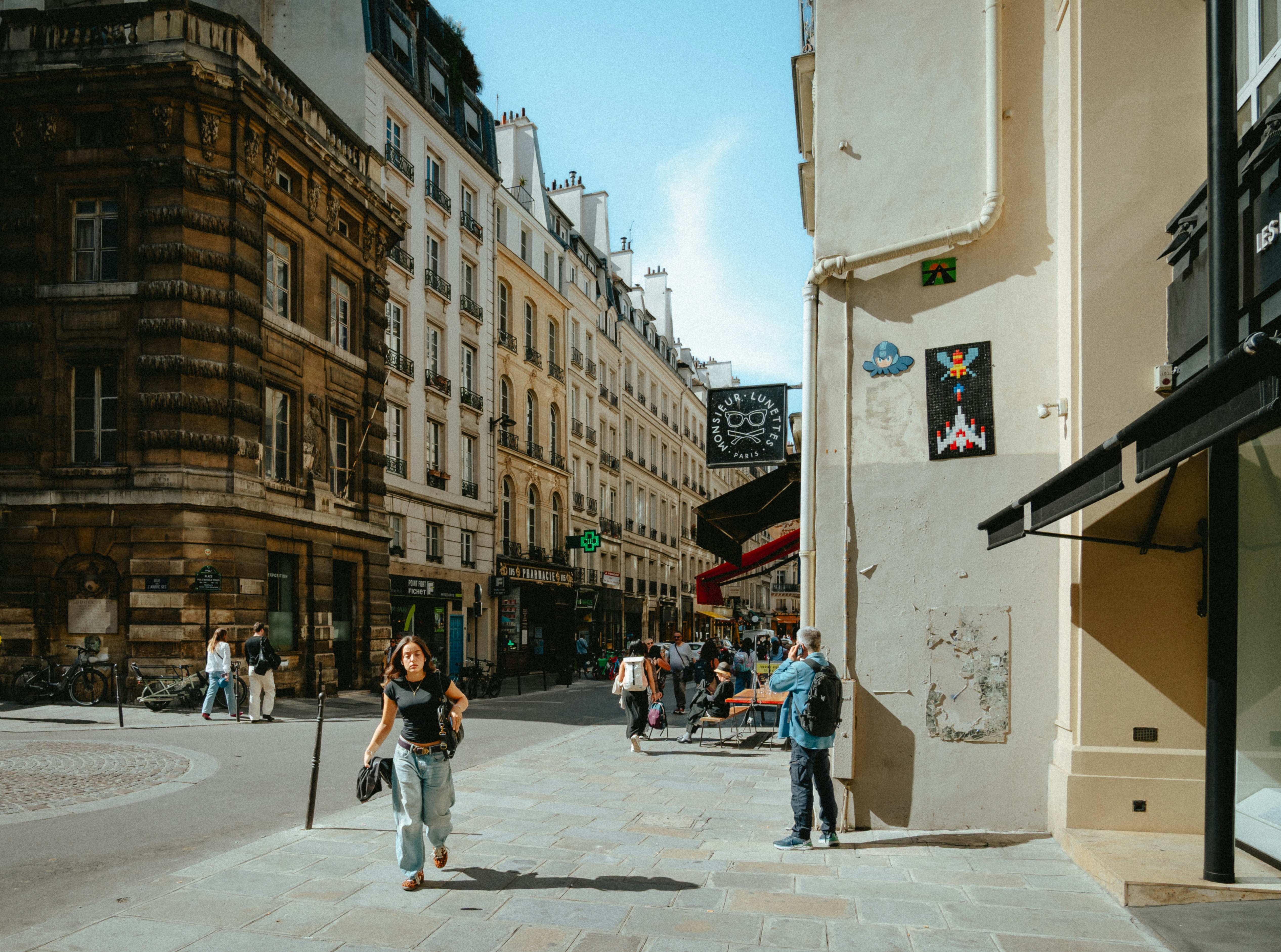 Sunlit city street with pedestrians and classic architecture; a casual scene capturing daily life beside a storefront mural.