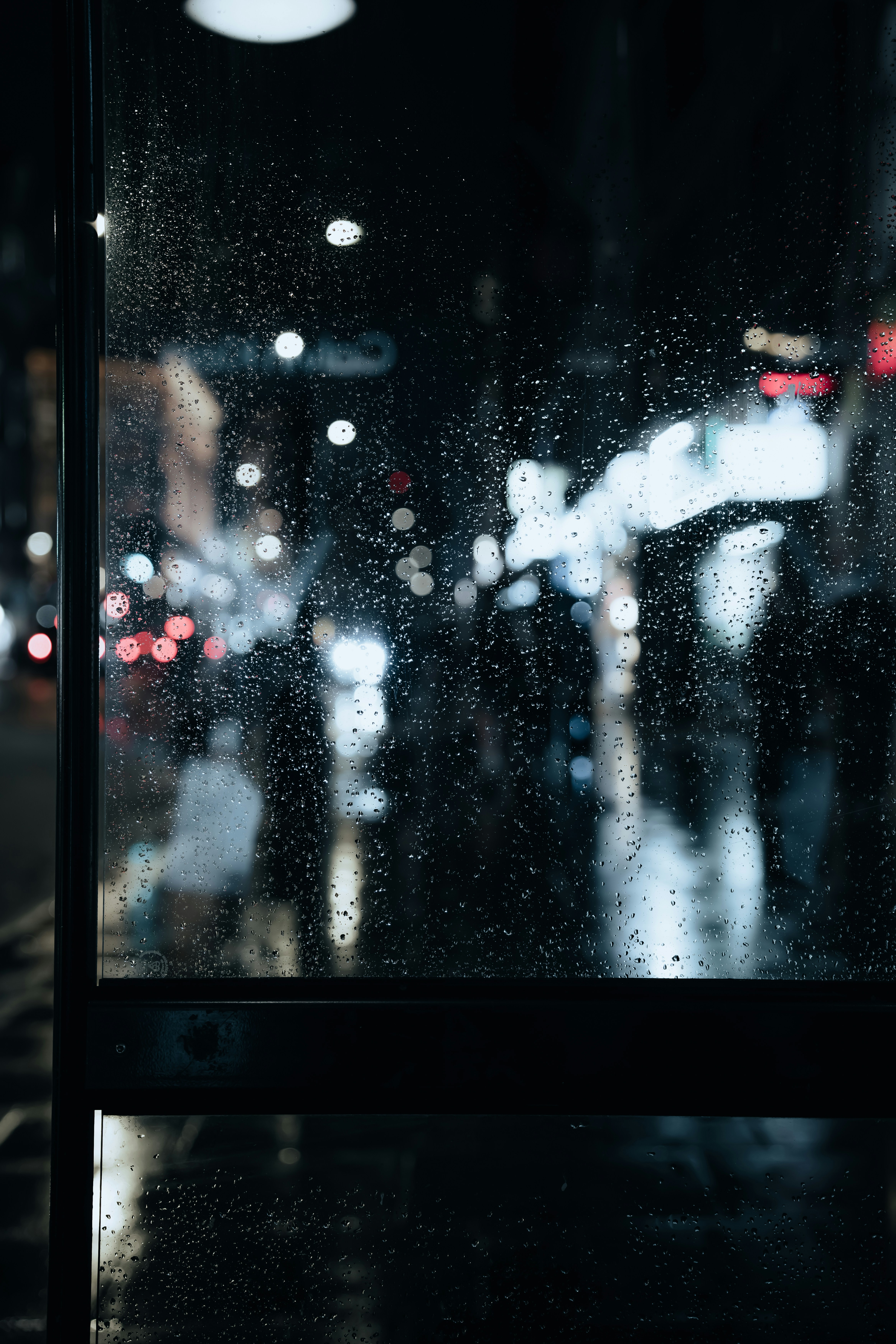 Rain-streaked Night Reflections in a City Bus Stop Window