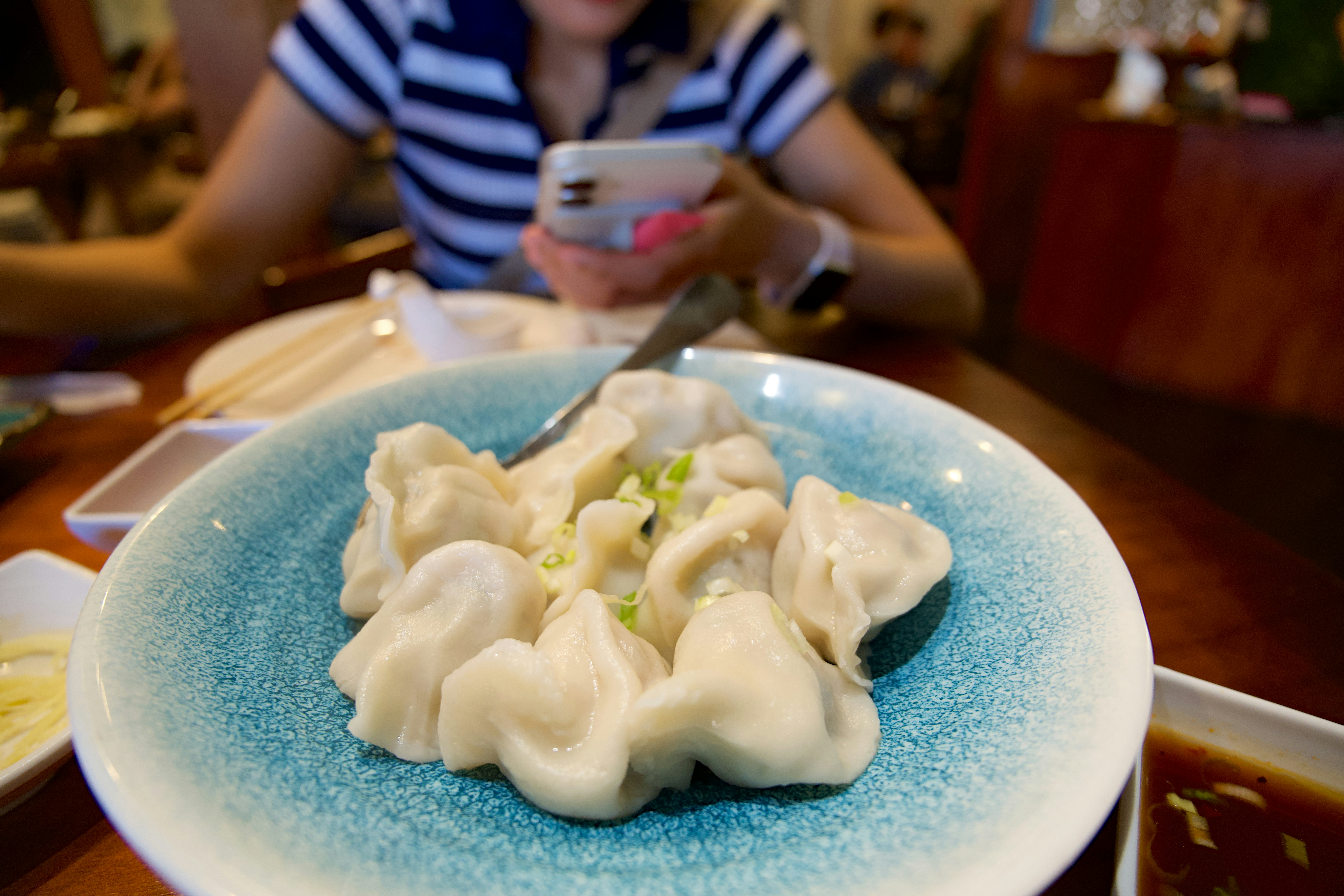 Dumplings on a blue plate with a striped-clad diner in the background