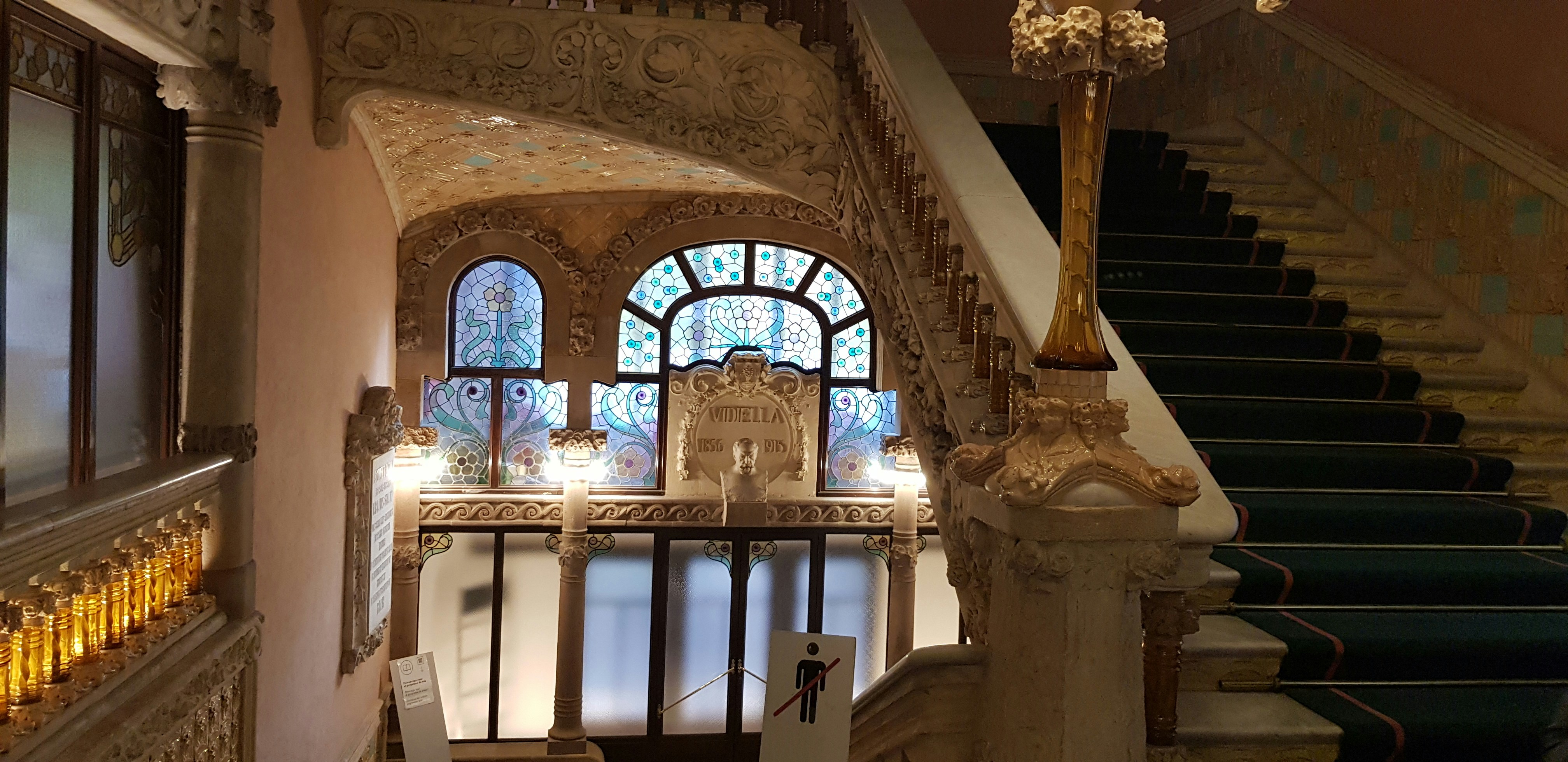 Intricate stairway, carved balustrades and stained glass above a grand entry, capturing the architectural richness of a historic interior.