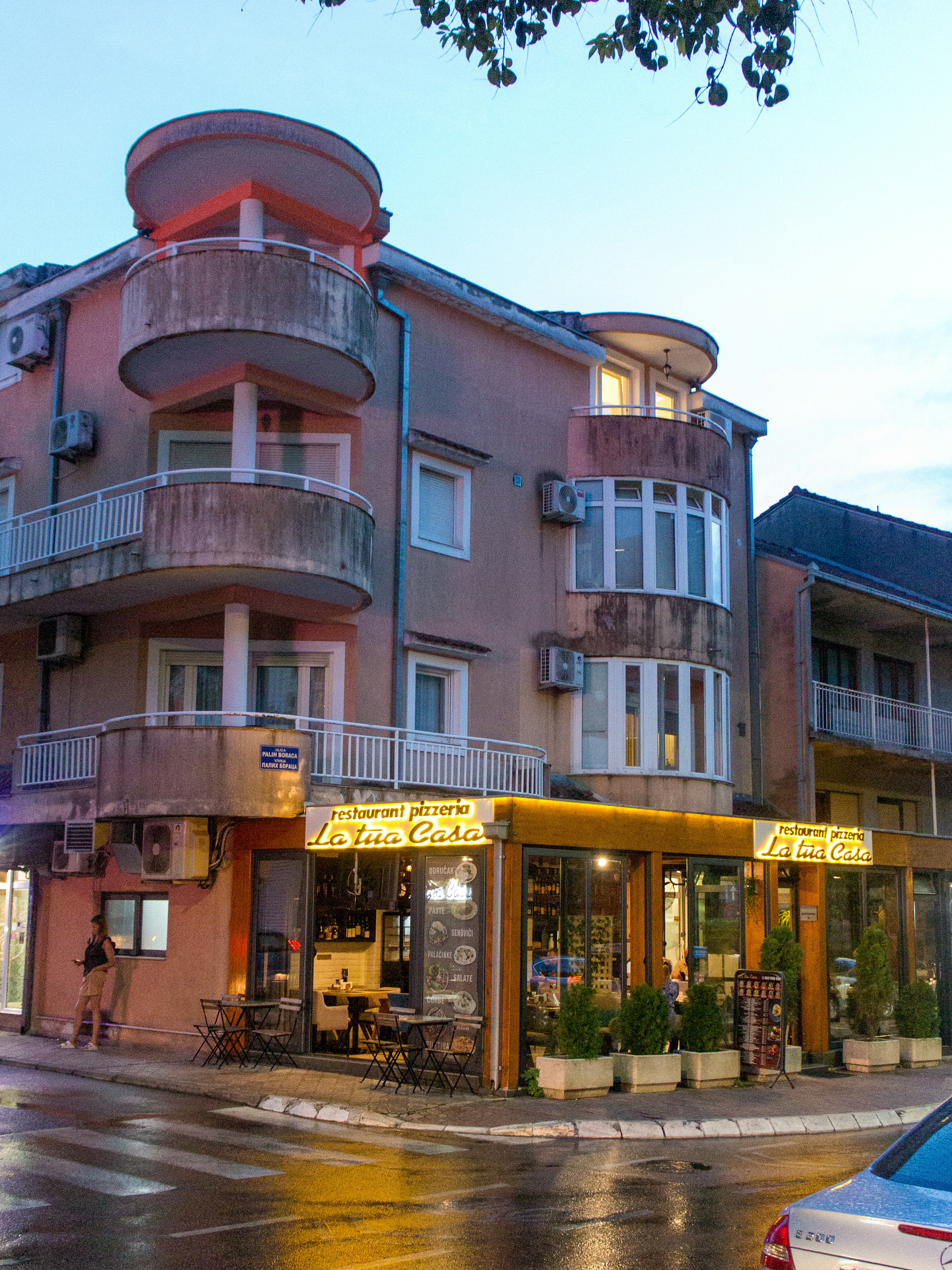 Neon-lit pizzeria at the corner of a pastel apartment block