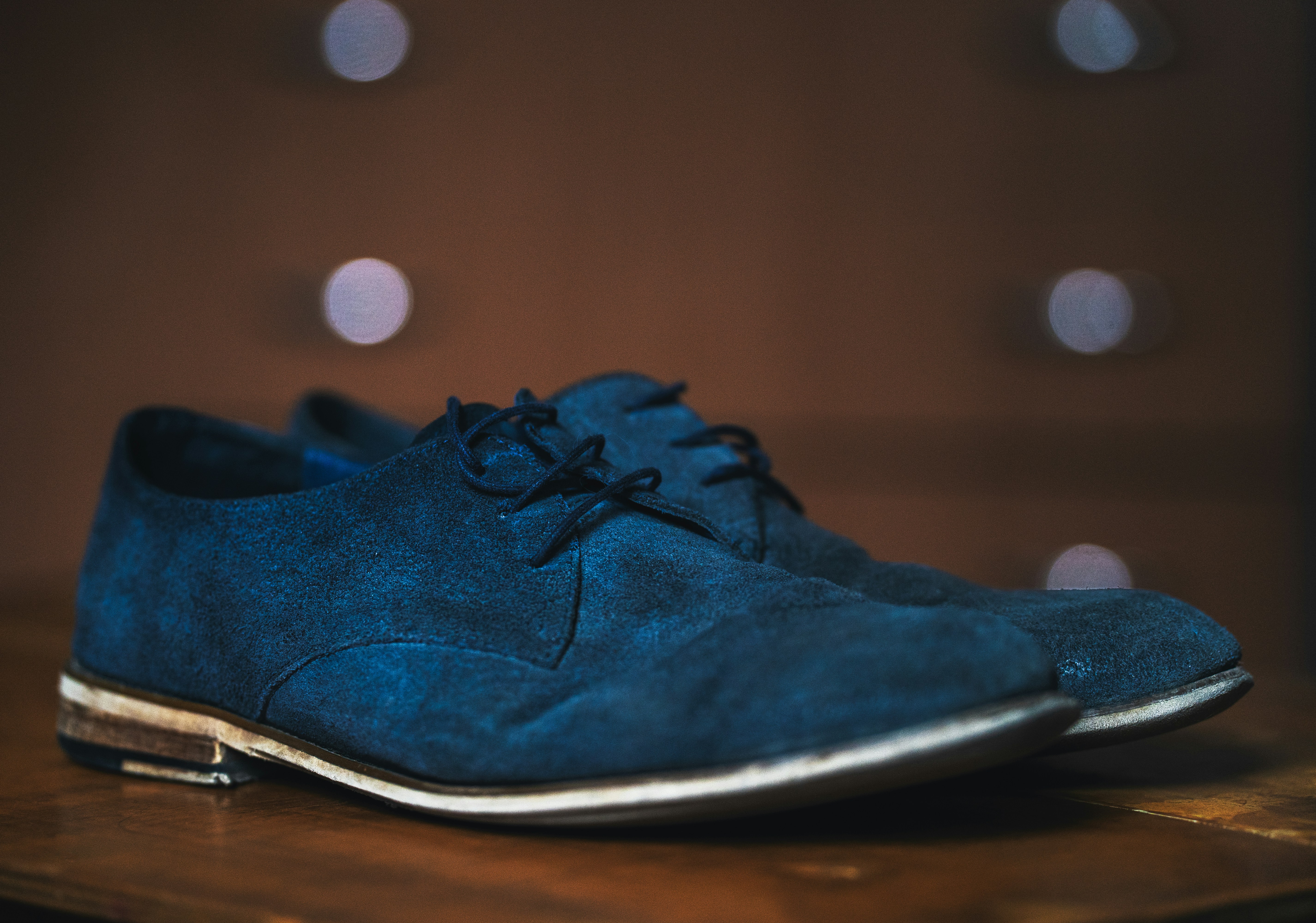 Blue suede oxford shoes resting on a wooden surface with soft bokeh background; a still life emphasizing texture and color of the footwear.