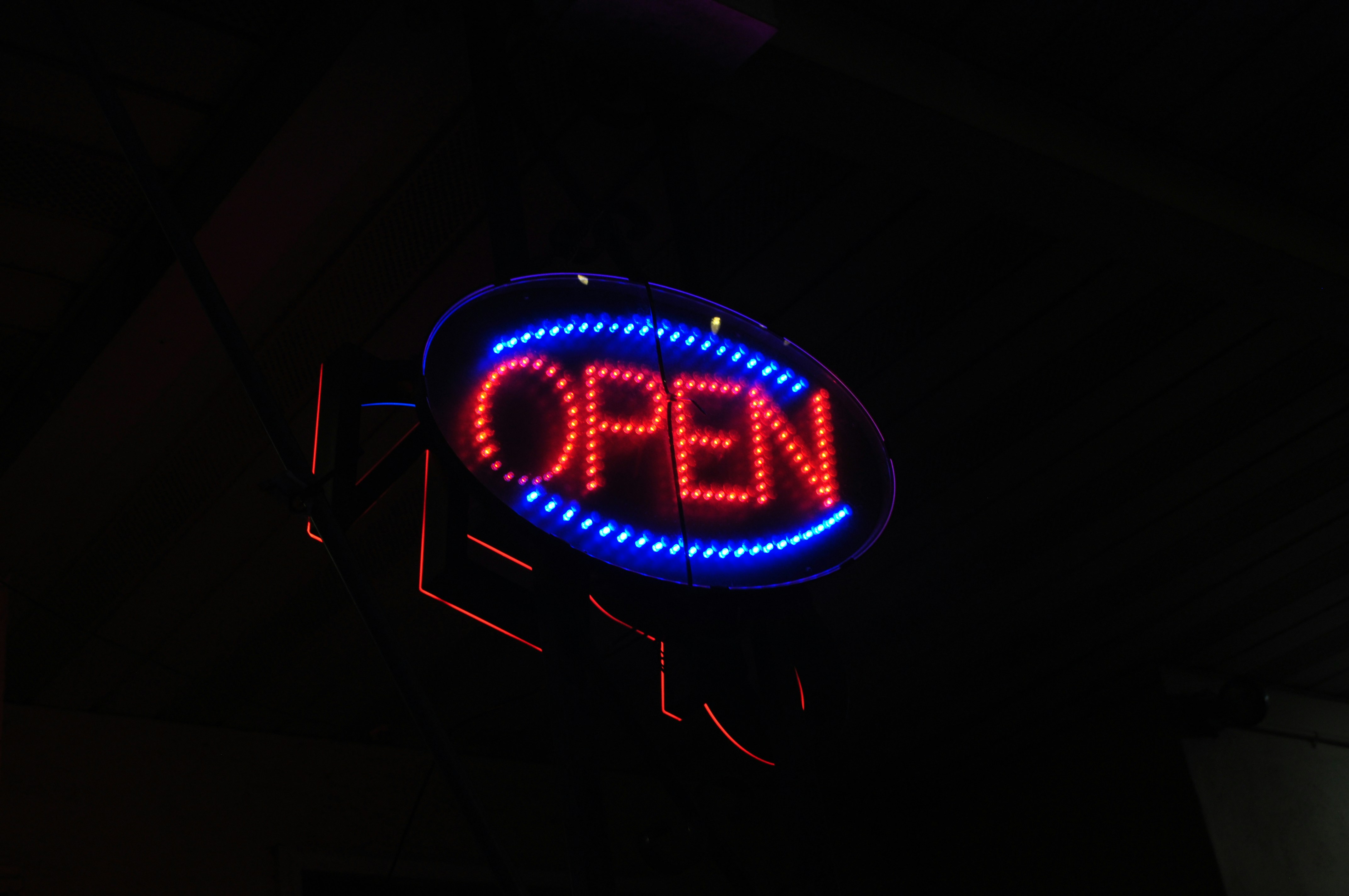 Bright blue-and-red neon OPEN sign hangs in a dark indoor space, its glow casting subtle reflections and outlining a moody, intimate atmosphere.