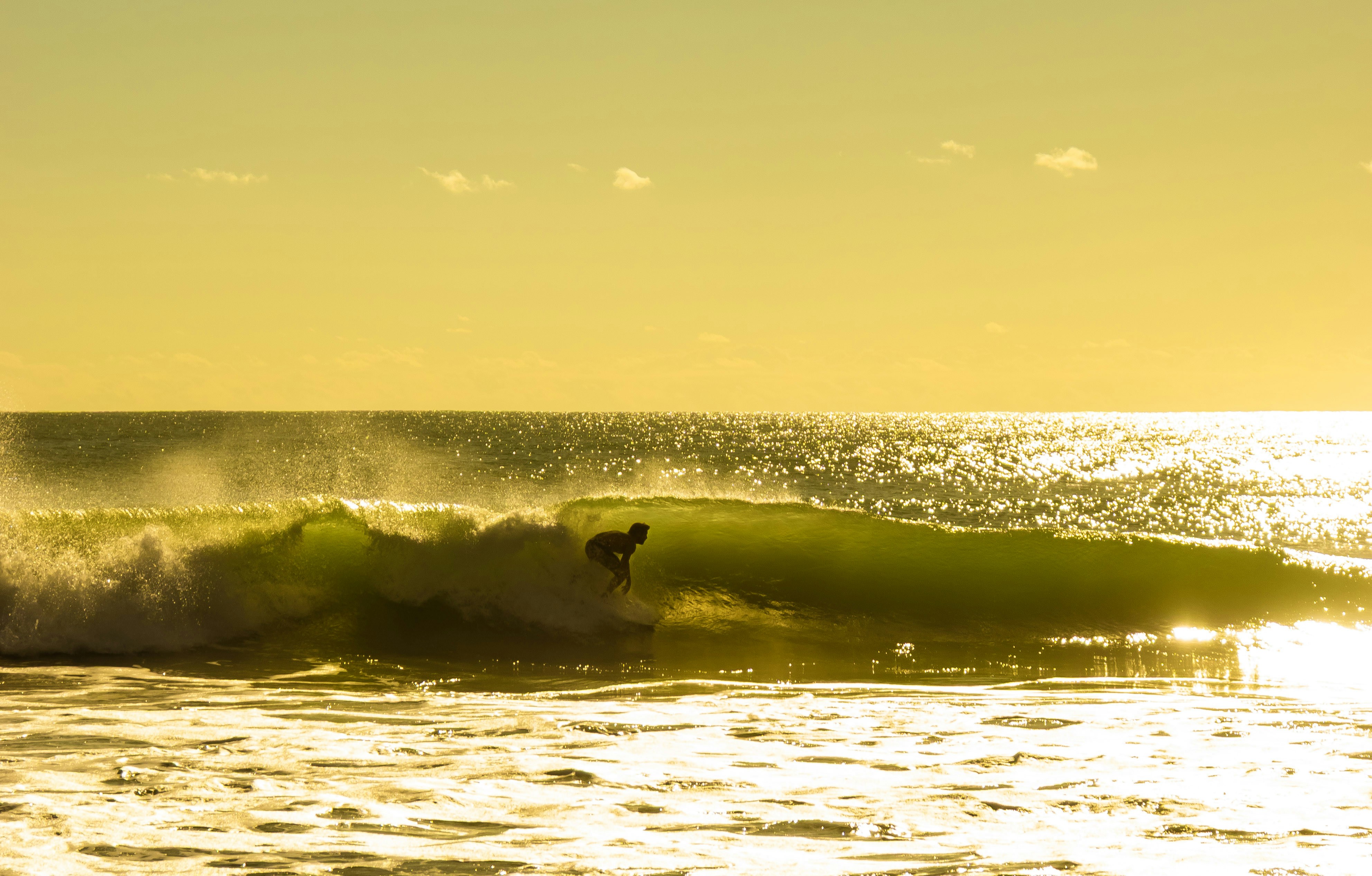A surfer riding a wave in the ocean under a bright golden sky