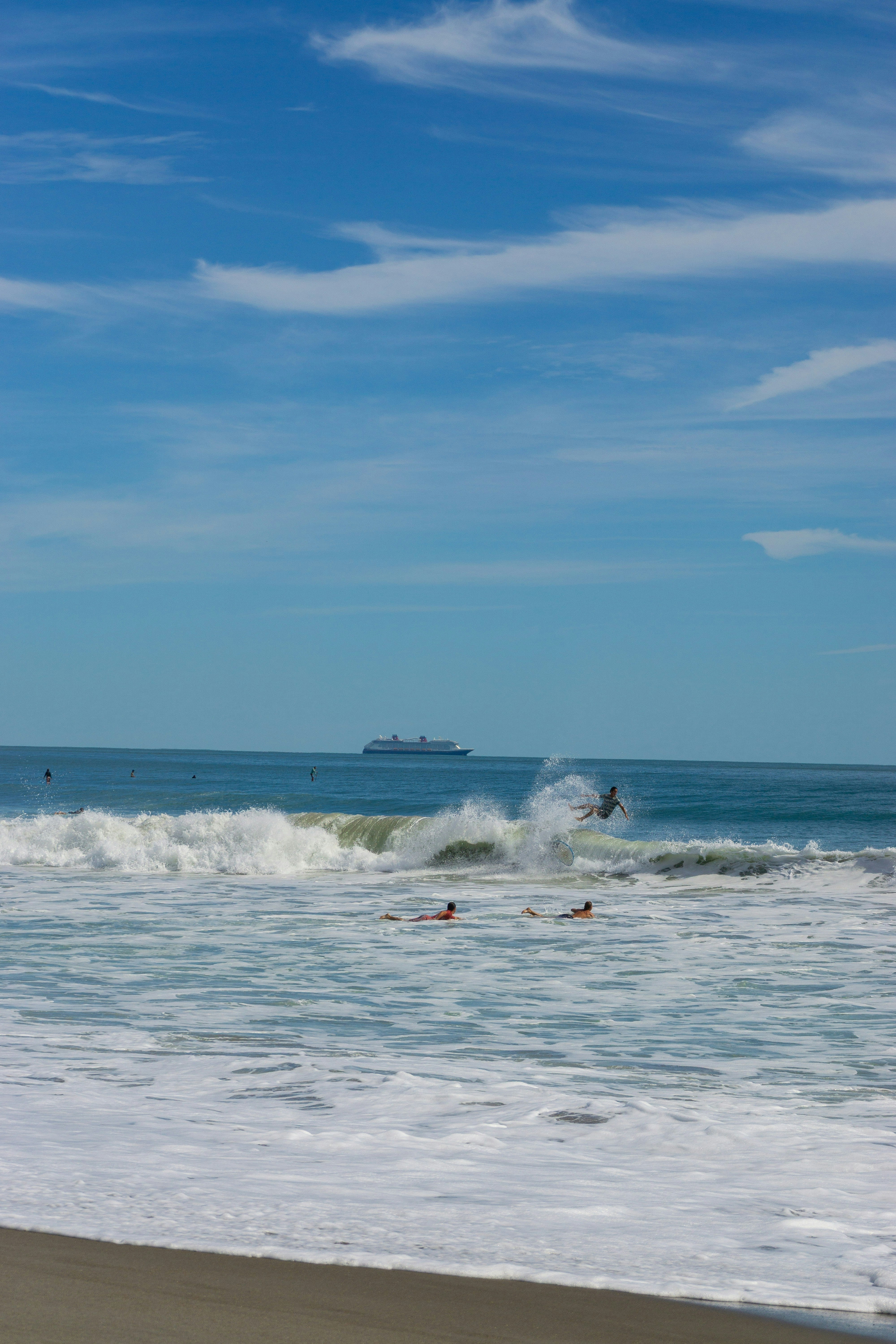 Crewed Horizon: Surfers and Ship on a Clear Coastal Day