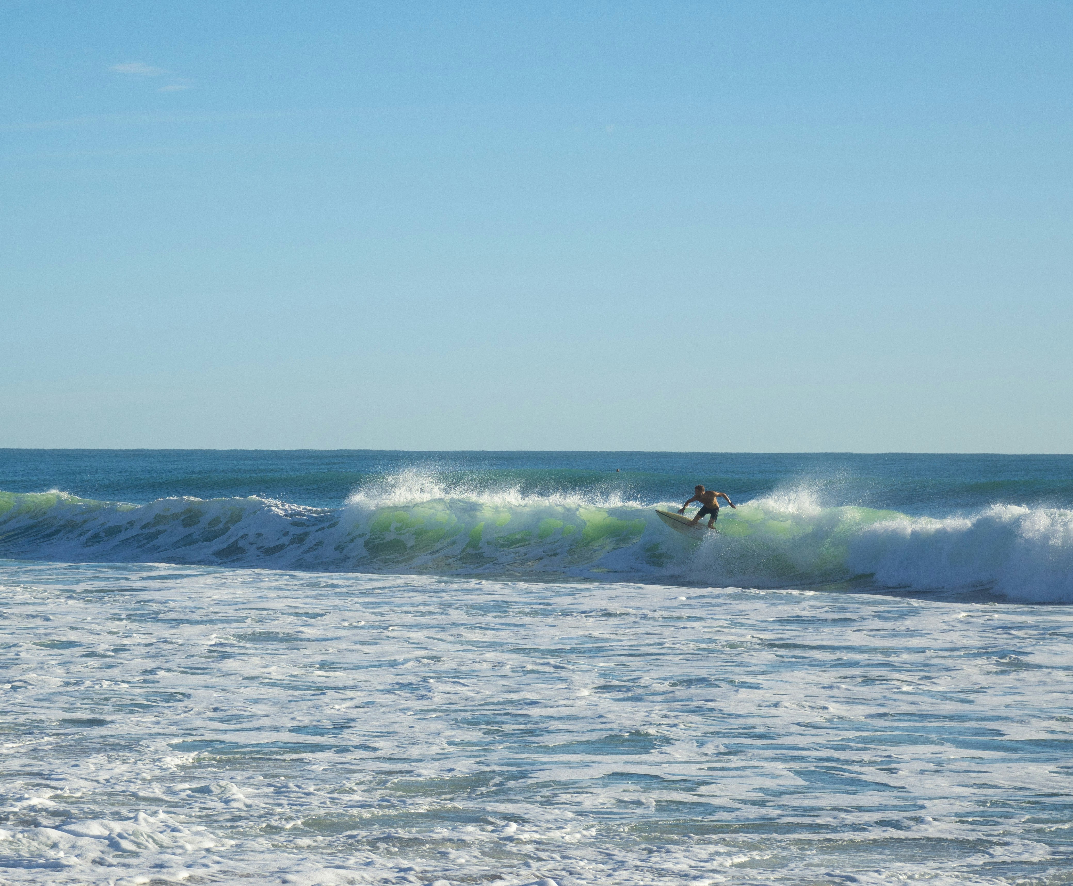 Surfer Riding a Green-Crested Wave at Distant Shore