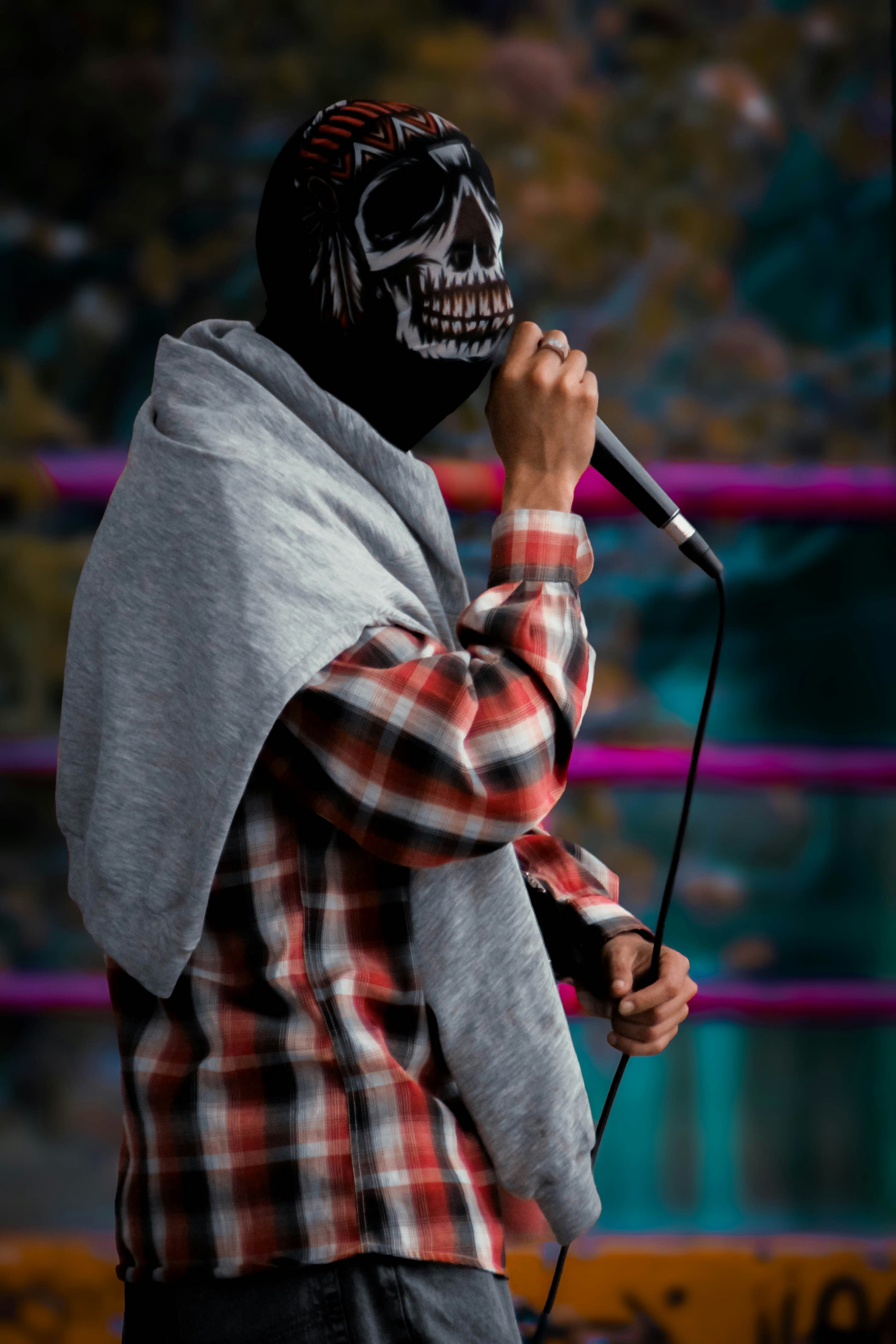 Masked singer on a dim stage: microphone grip and hooded skull motif