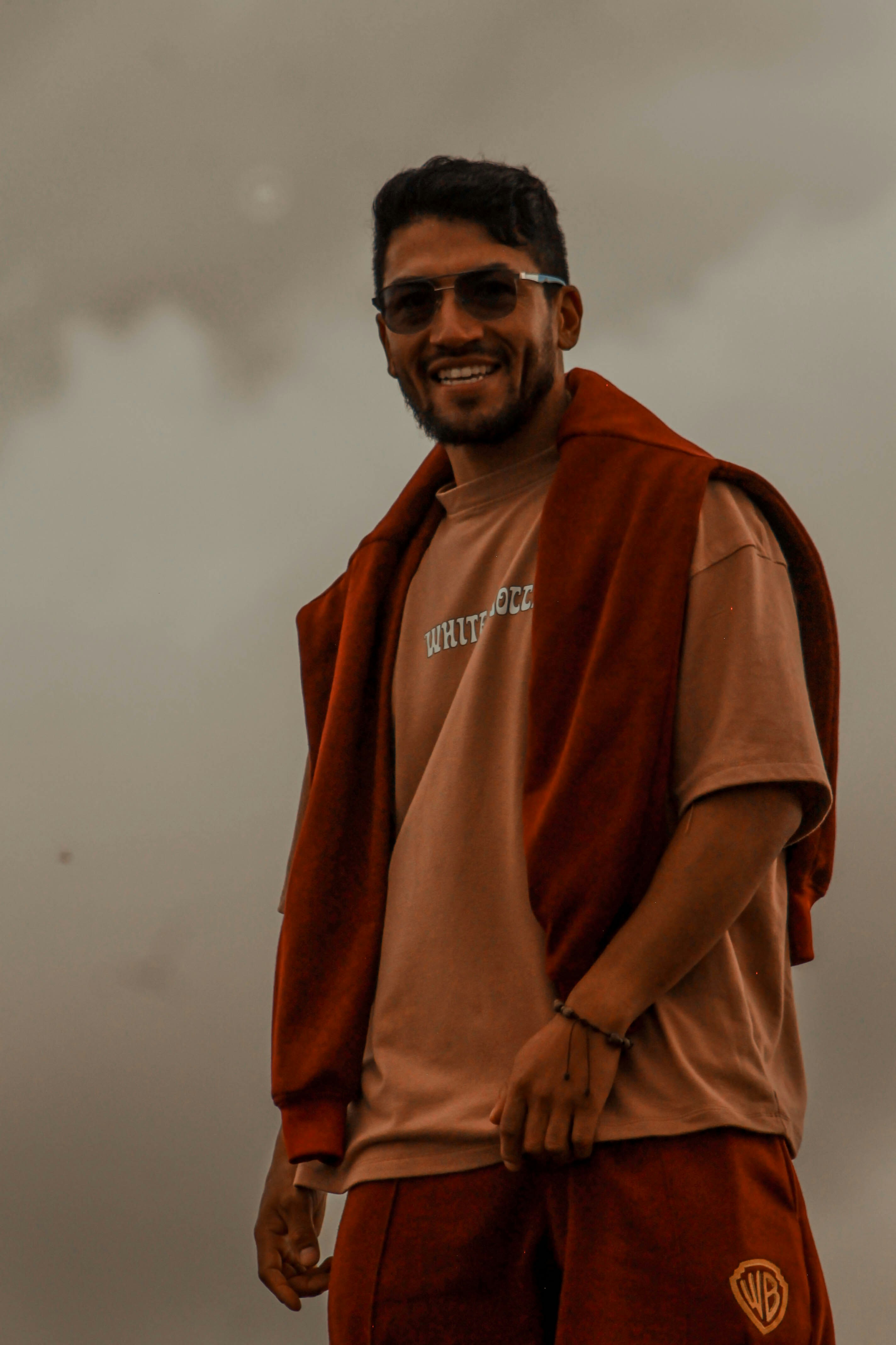 Smiling Confidence: Hoodie and Glasses Against a Stormy Sky