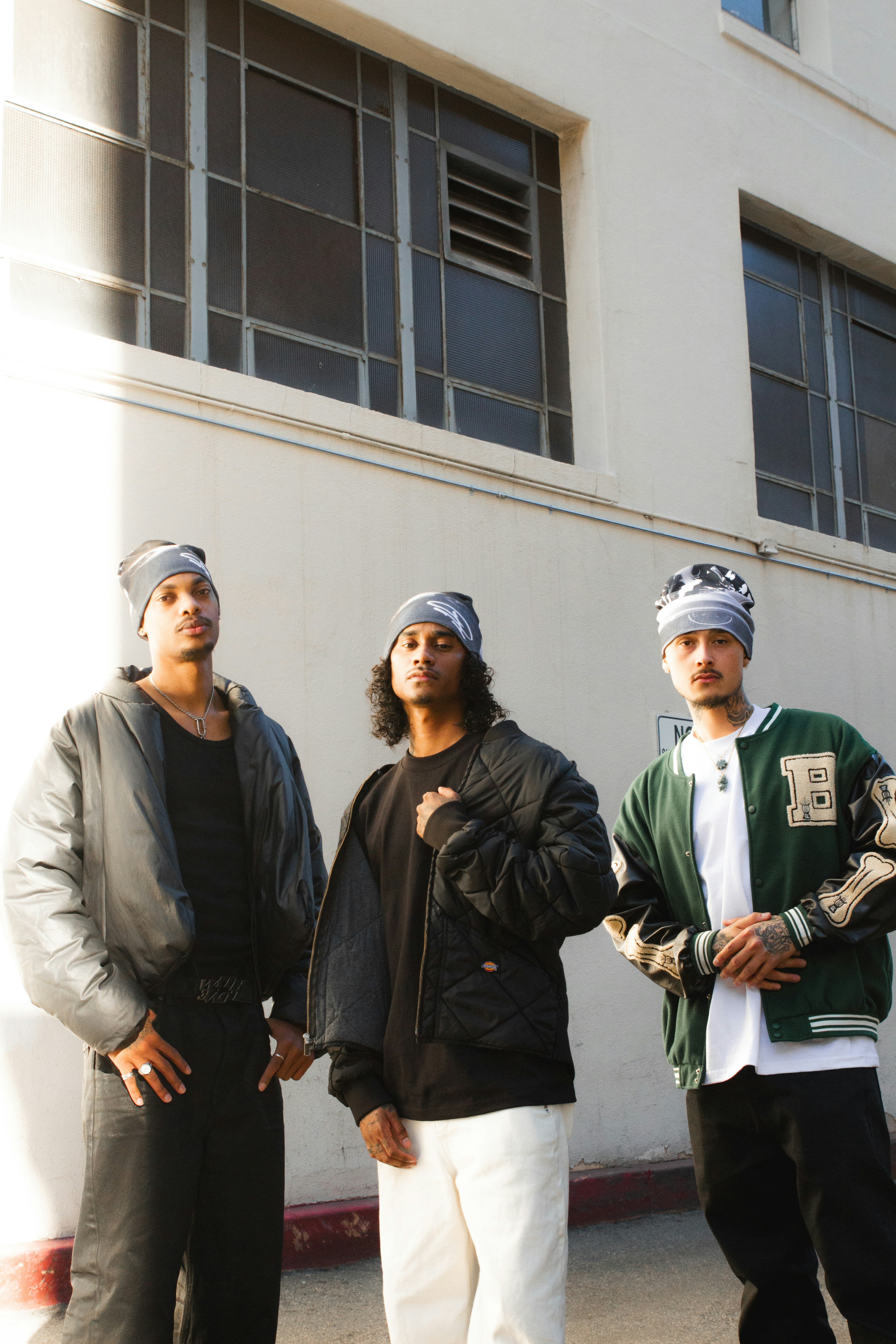 Three friends pose against a sunlit urban wall in coordinated casual wear