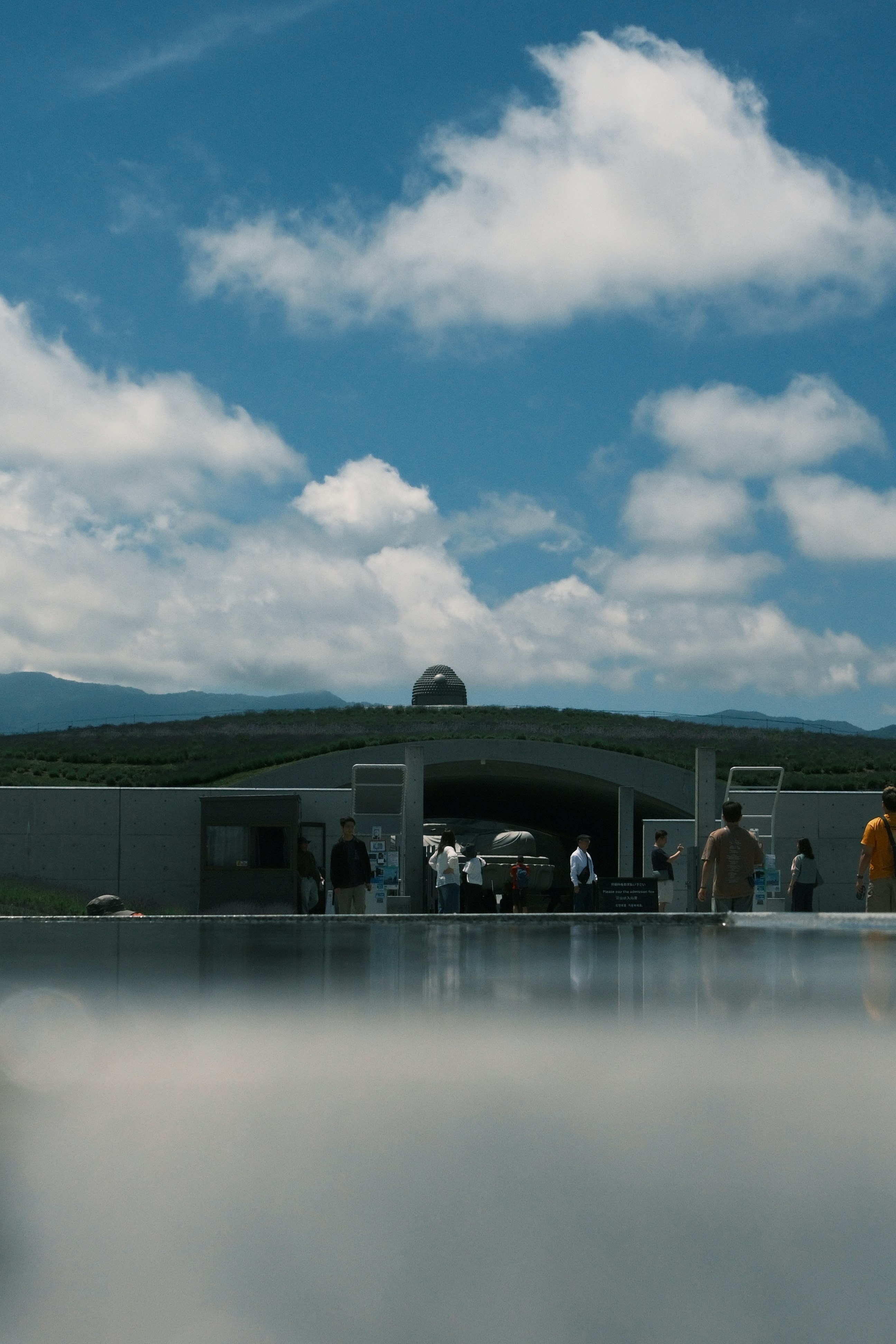 People entering a concrete tunnel structure with a domed roof under a blue sky