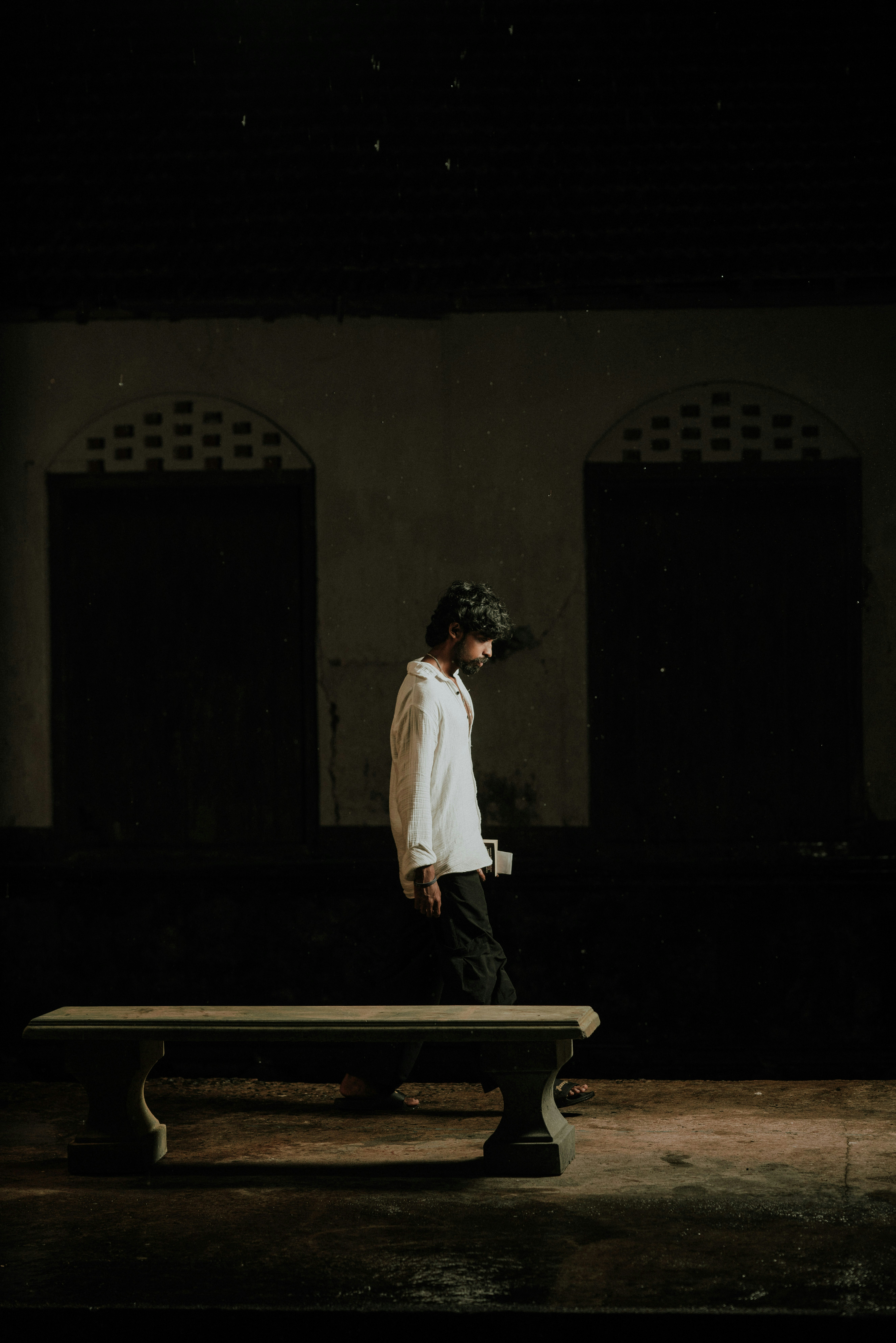 A man in a white shirt walking past a stone bench at night