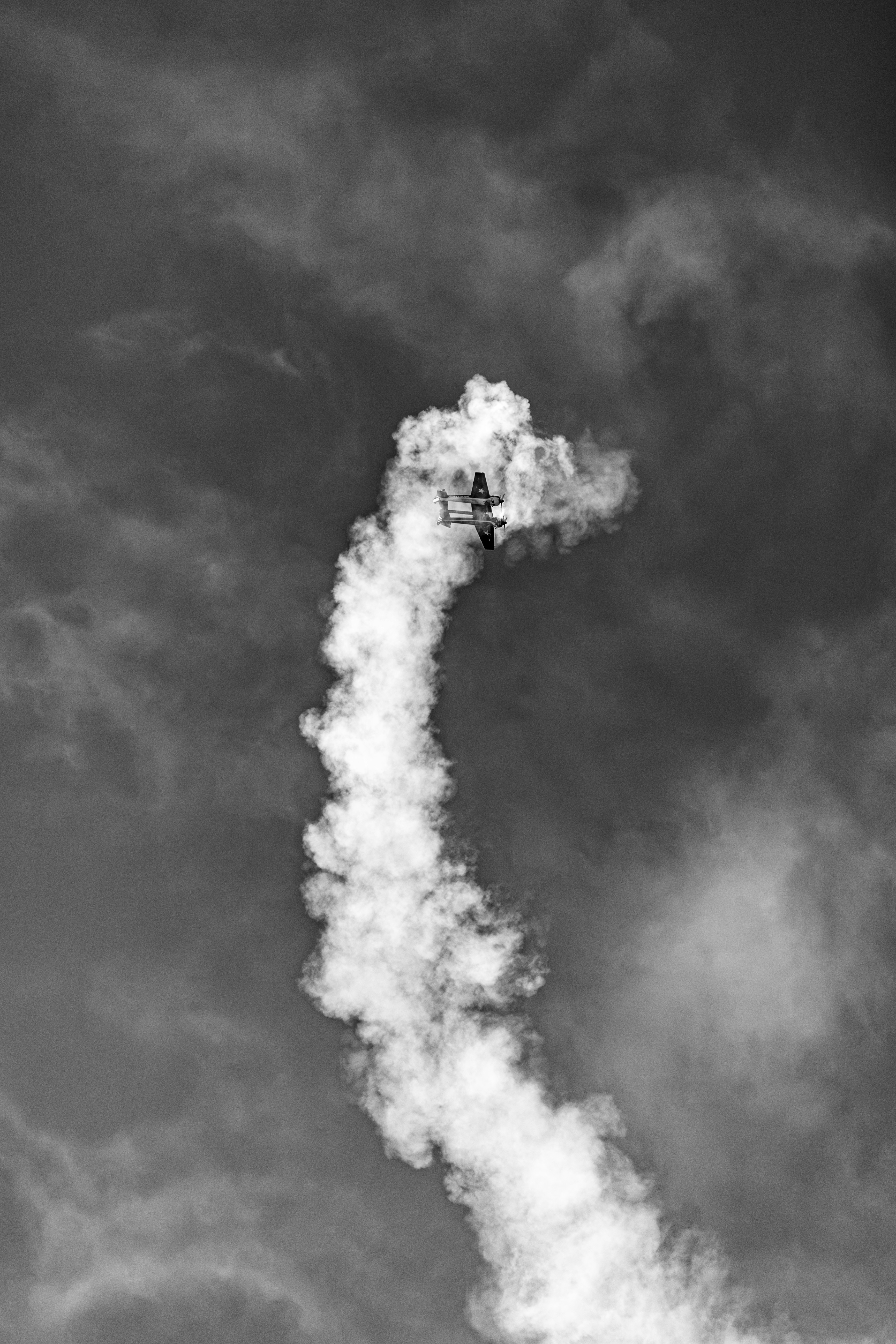 Smoke-curved ascent: a solo aerobatic plane carving a white arc against a moody sky