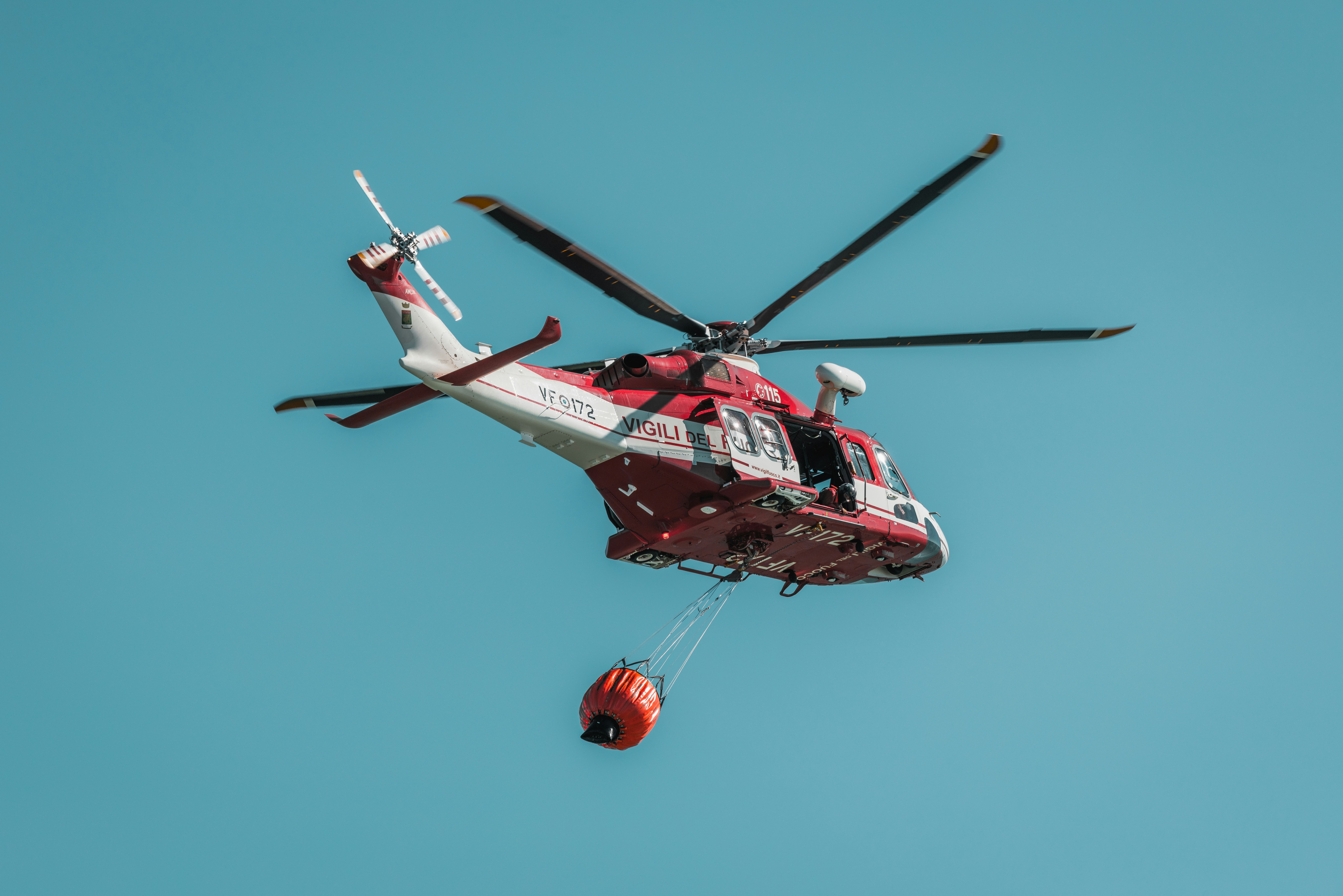 Red rescue helicopter lifting a blazing orange buoy against a cloudless blue sky