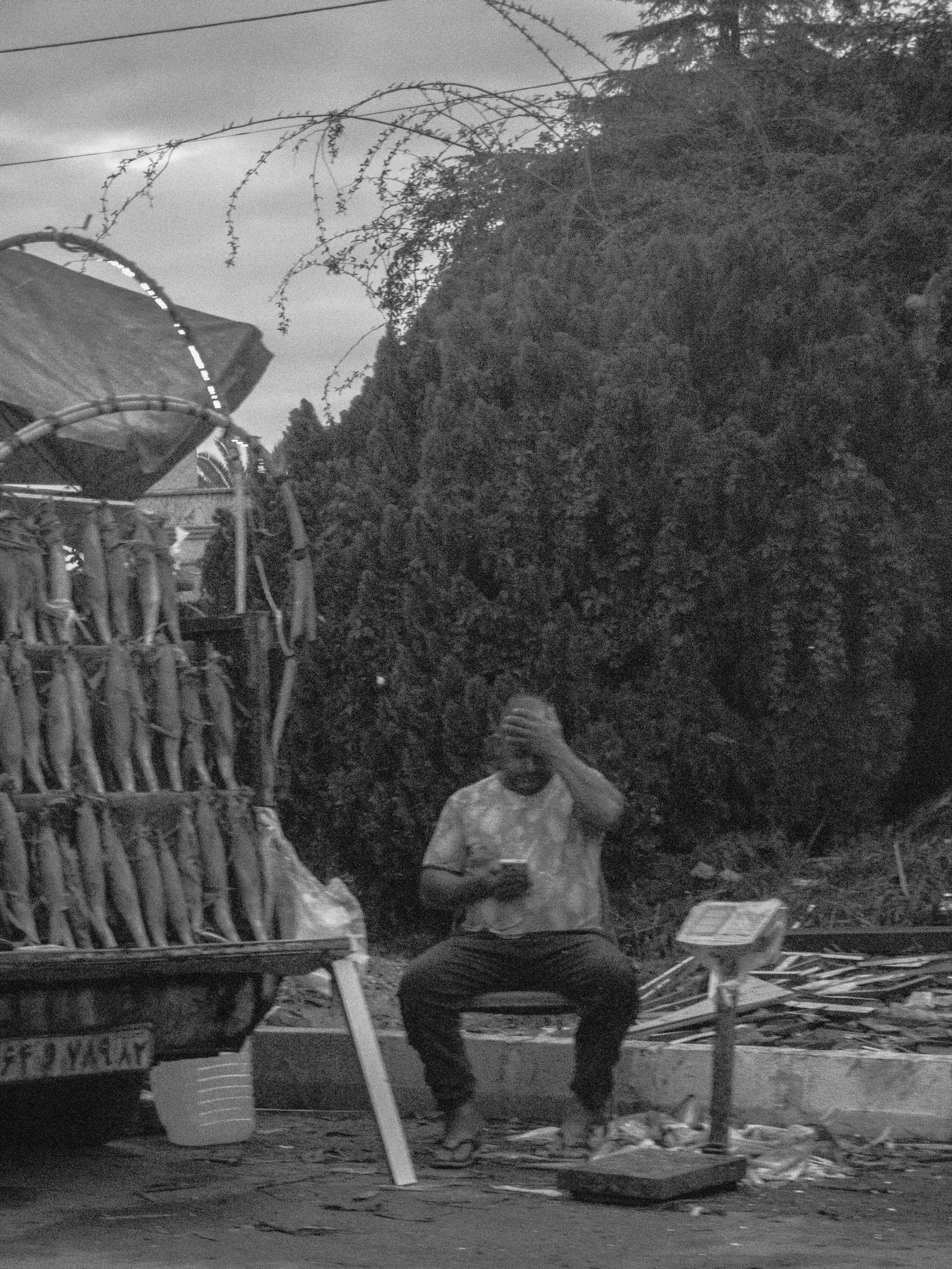 Grainy roadside vendor at dusk with a seated man in a makeshift setup