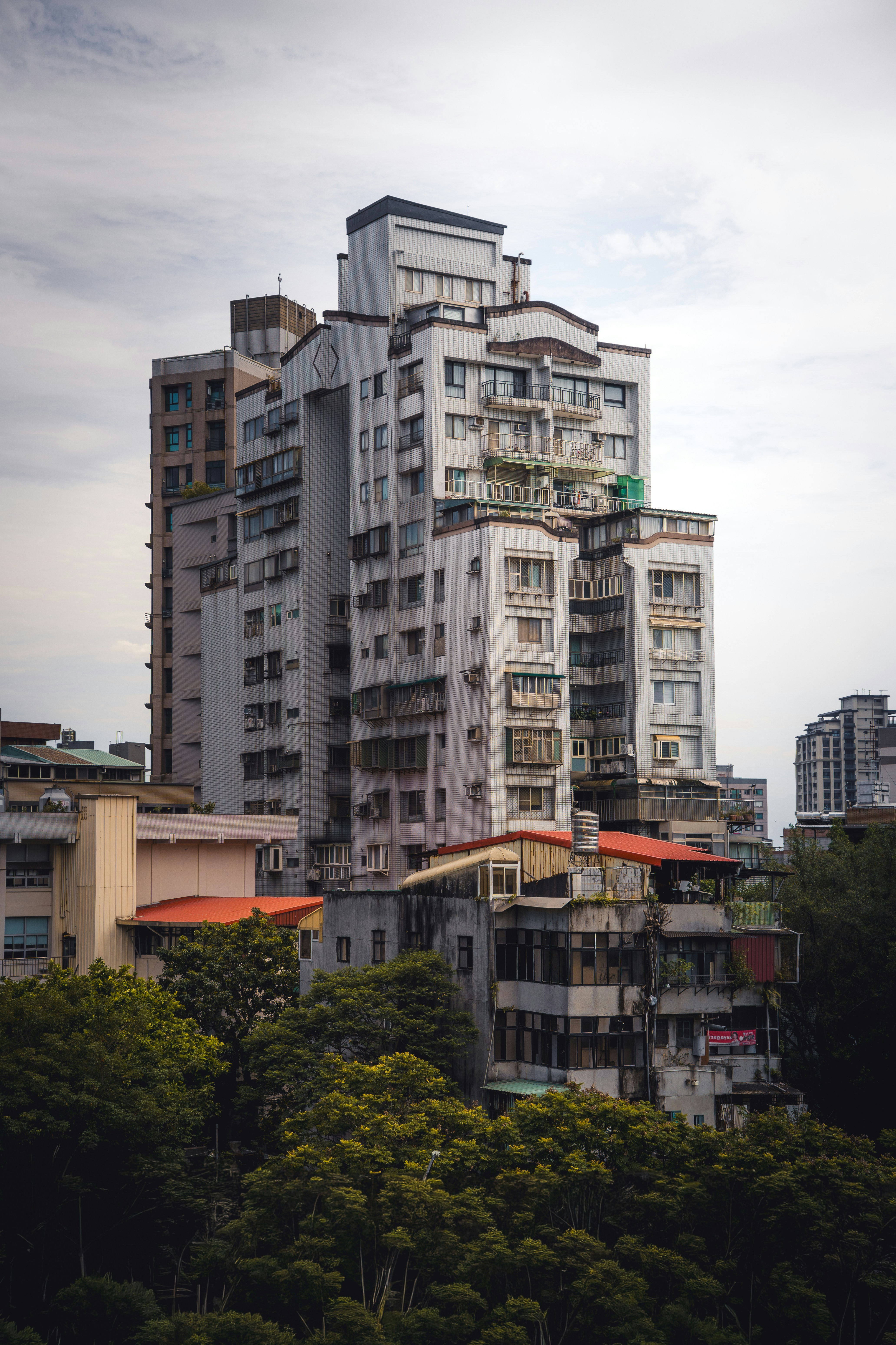 A multi-storey residential tower rises over a canopy of trees, with balconies and varied architecture giving a textured cityscape.
