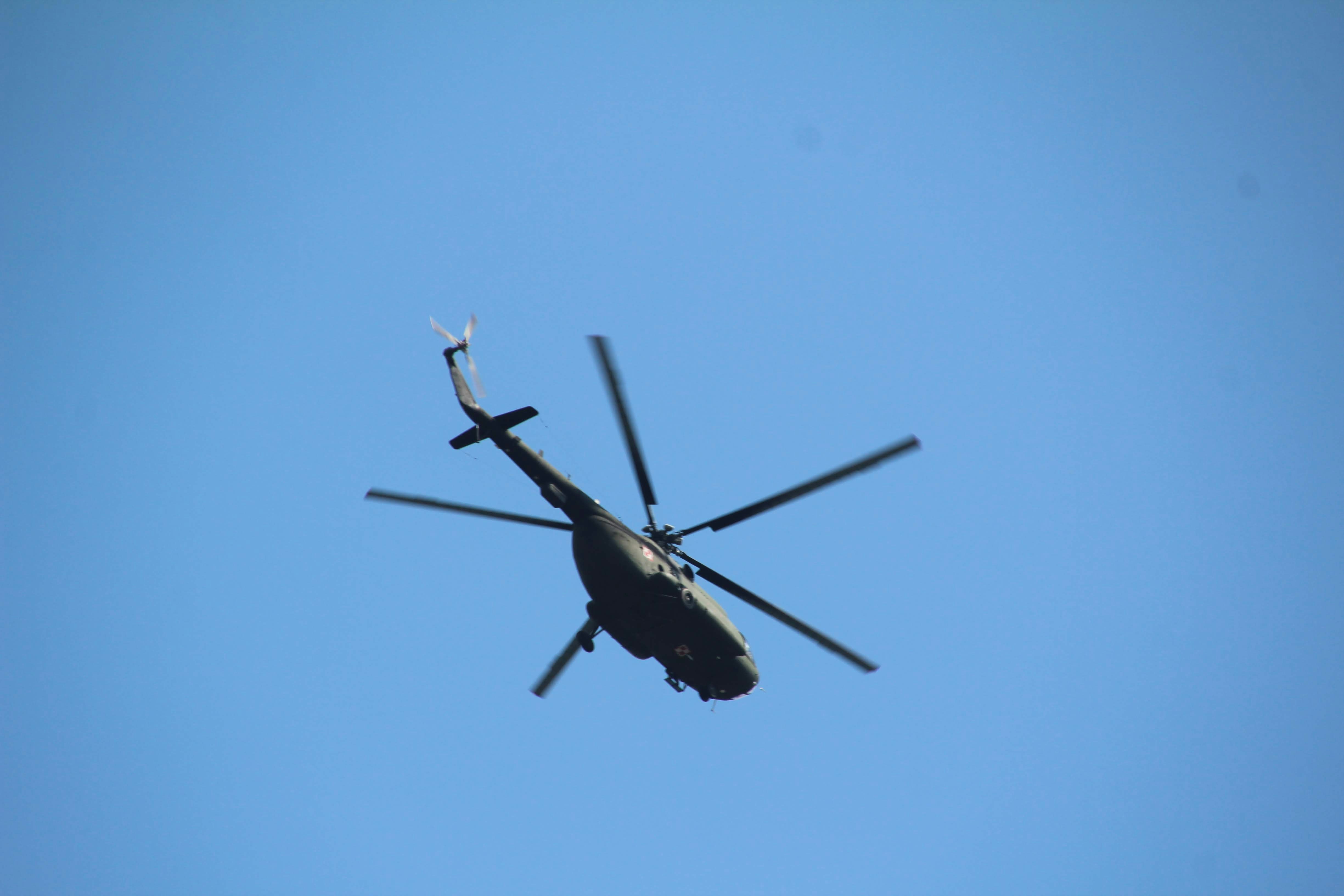 A dark green military helicopter flying against a clear blue sky