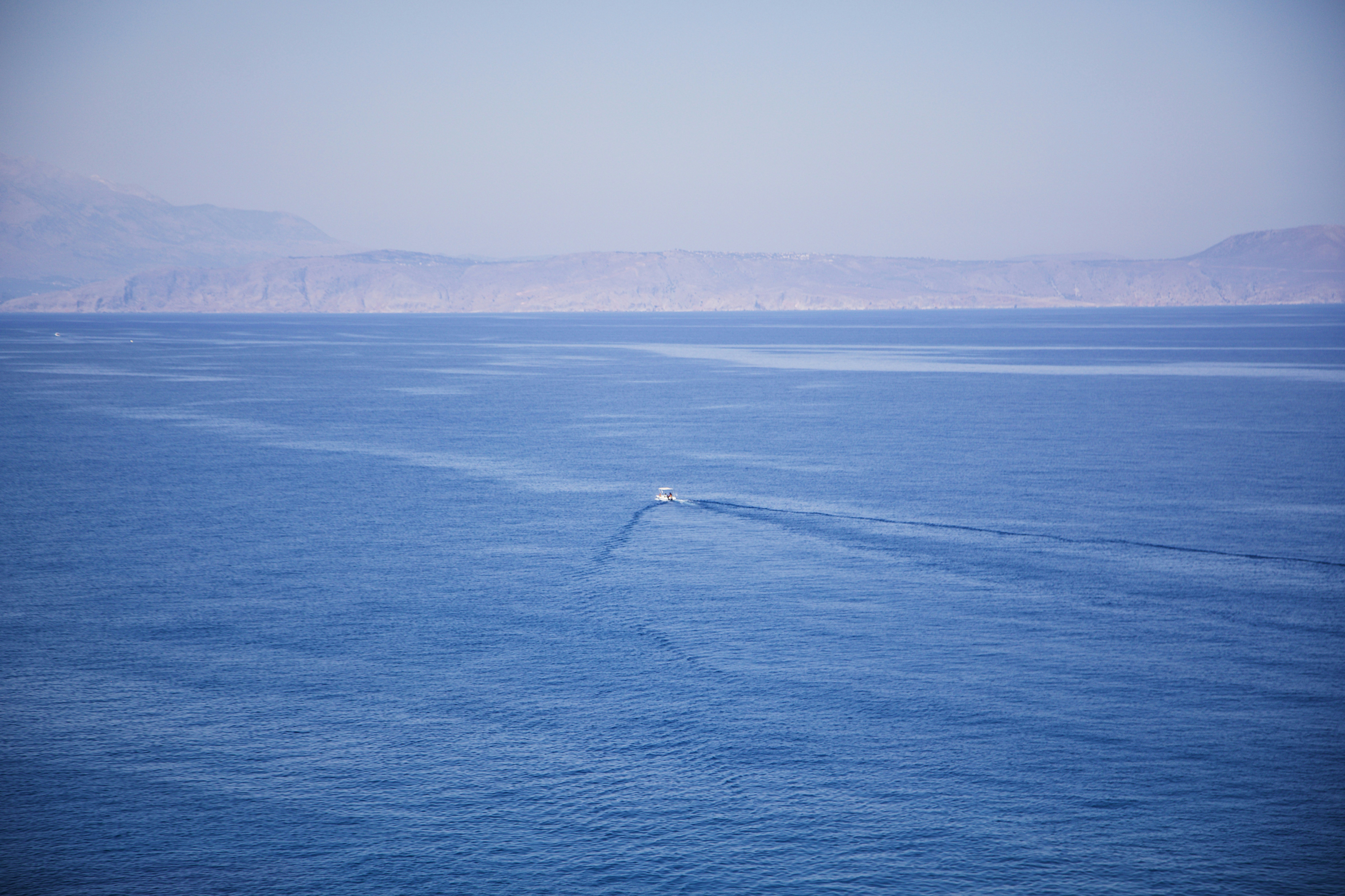 Boat Carves a Quiet Wake Across a Distant Blue Expanse